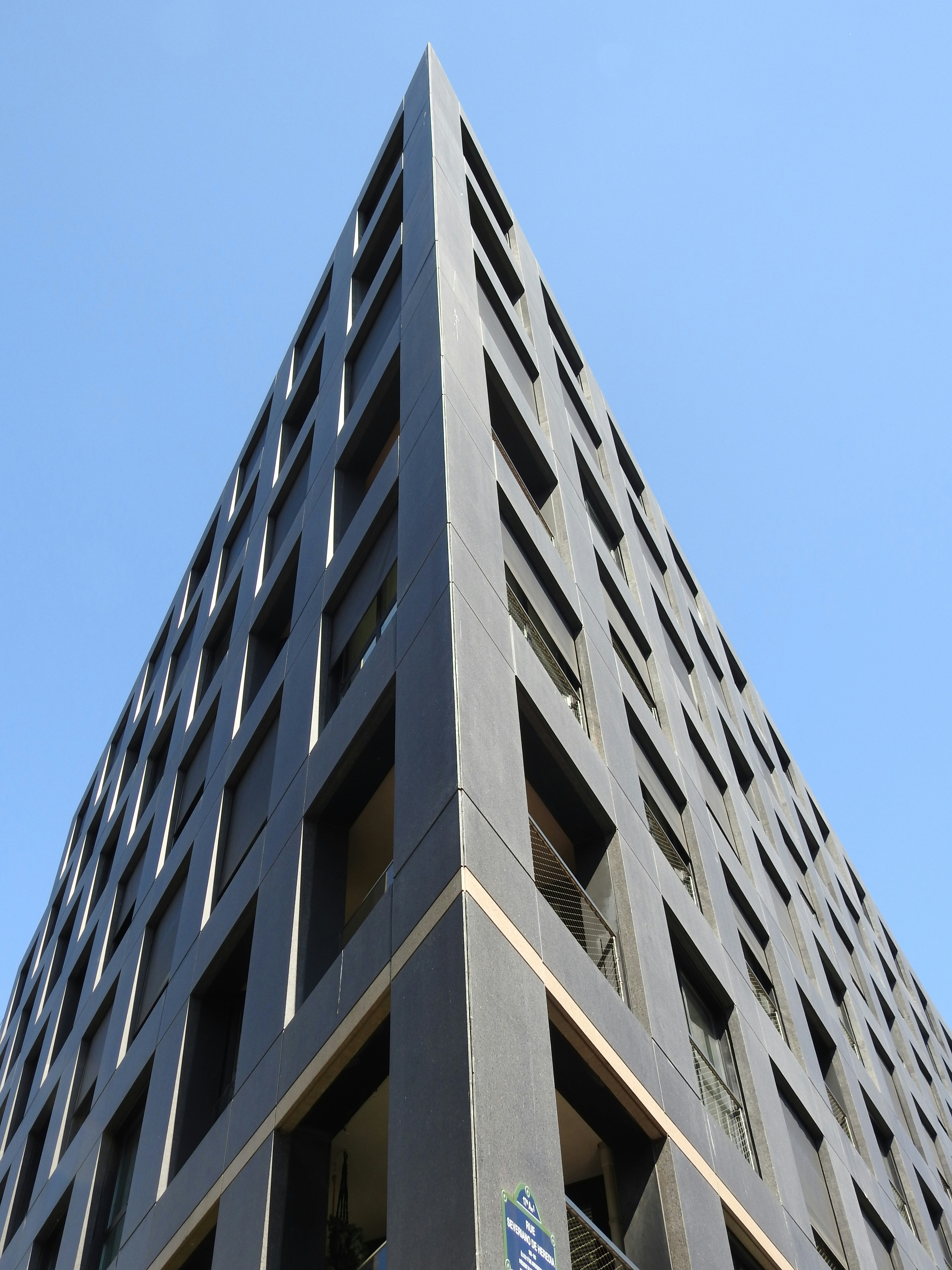 A sleek, modern building captured from a low angle, emphasizing its sharp lines and geometric design against a clear blue sky.