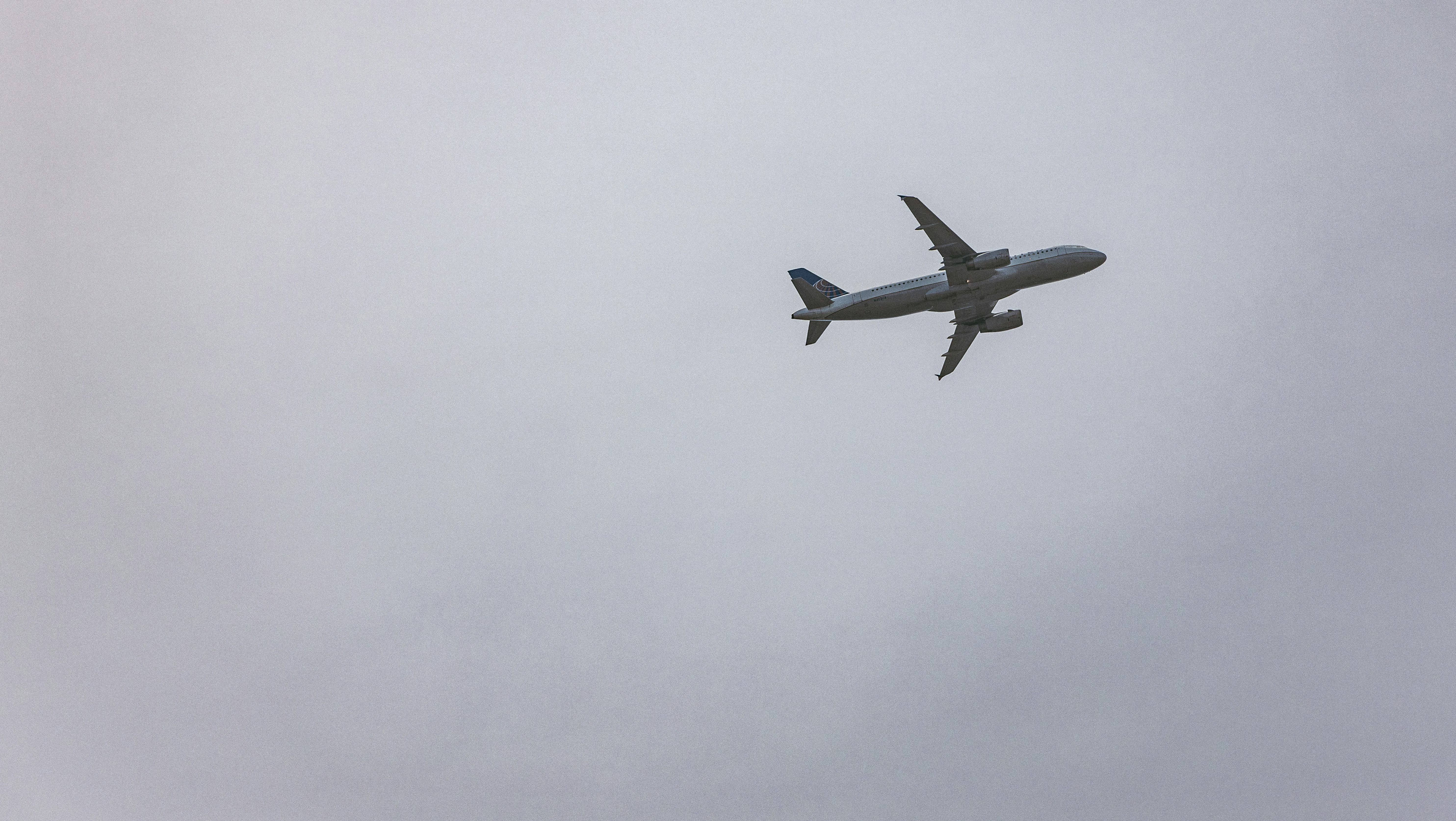 Commercial airplane gliding through a cloudy sky, showcasing the contrast between the aircraft and the muted backdrop.