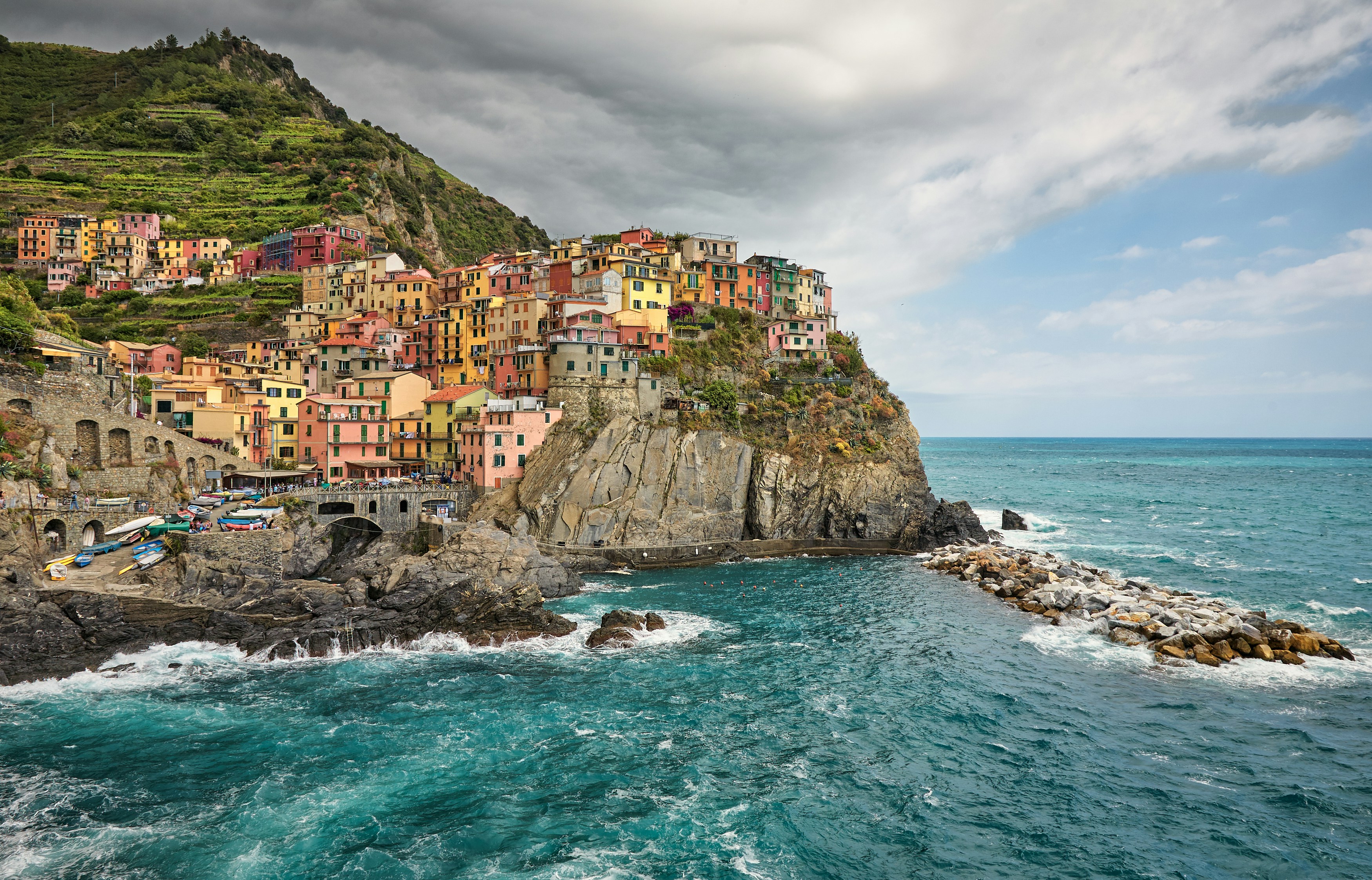 Vibrant hillside village perched on rocky cliffs above a turquoise sea under a dramatic sky.