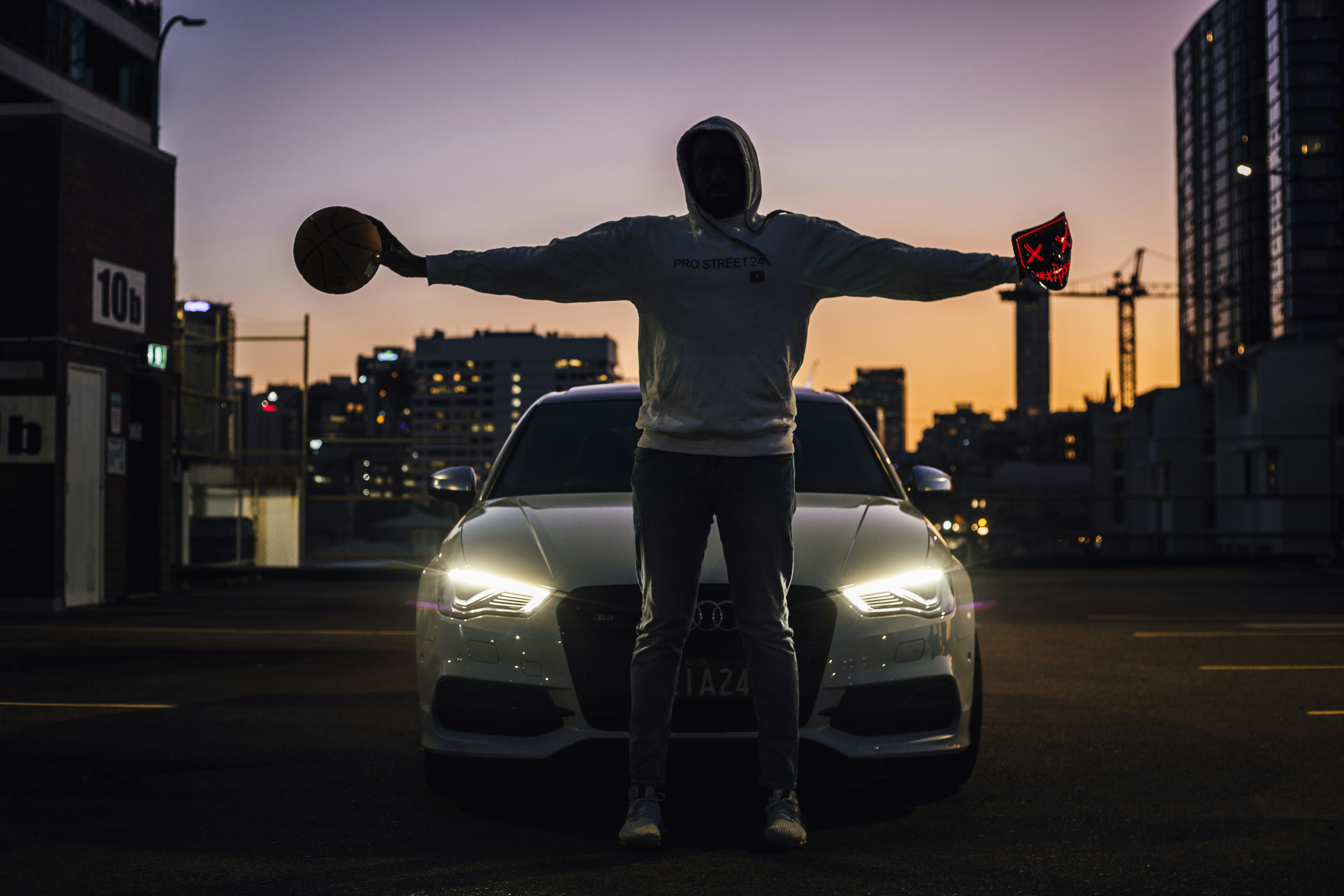 Silhouette at Dusk: A Hoodie Figure Framed by Headlights Against an Urban Sunset