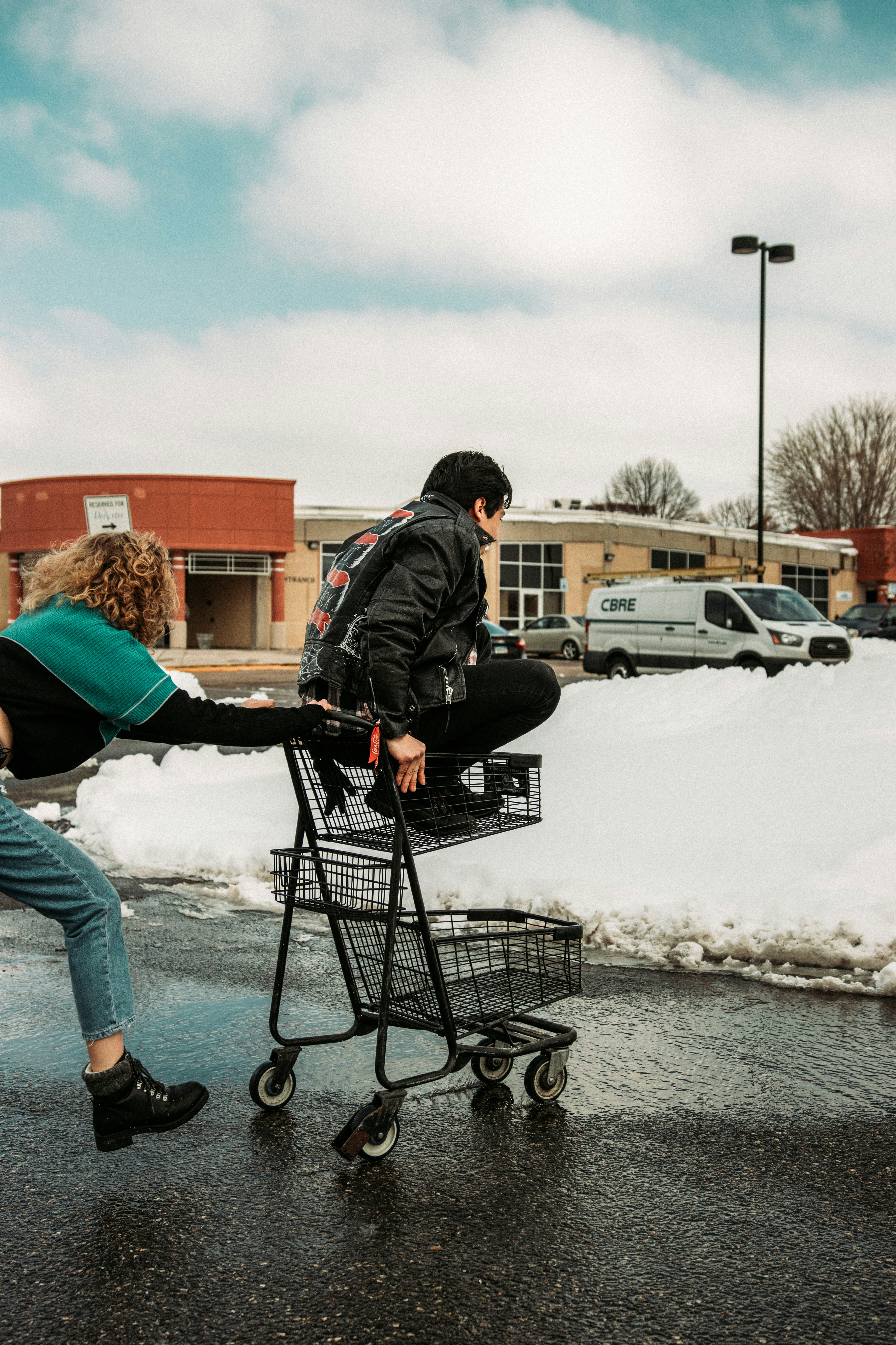 Snowy Retail Ride: A Rider on a Shopping Cart Escorted by a Friend