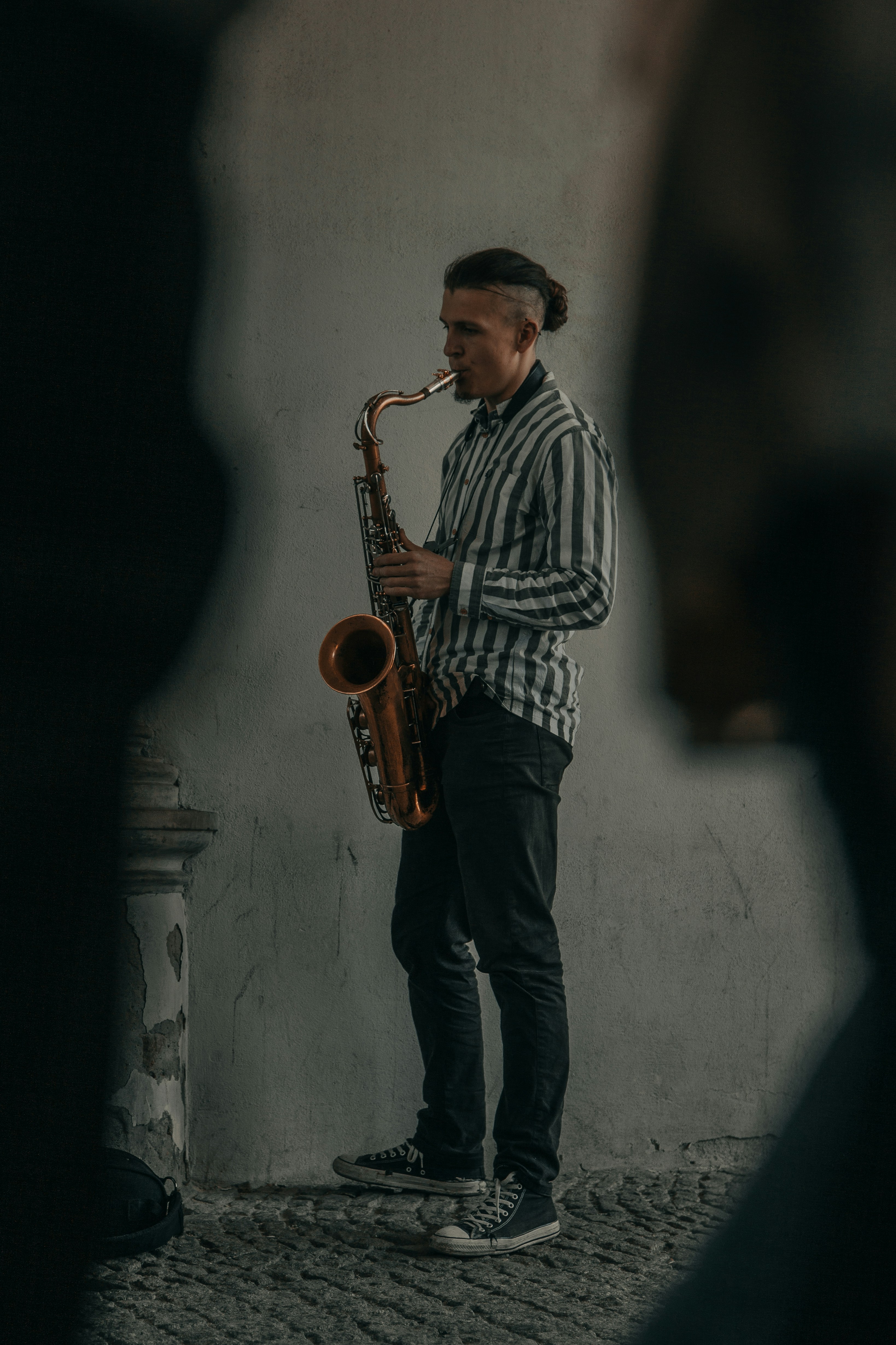 man in black and white striped long sleeve shirt and black pants holding saxophone