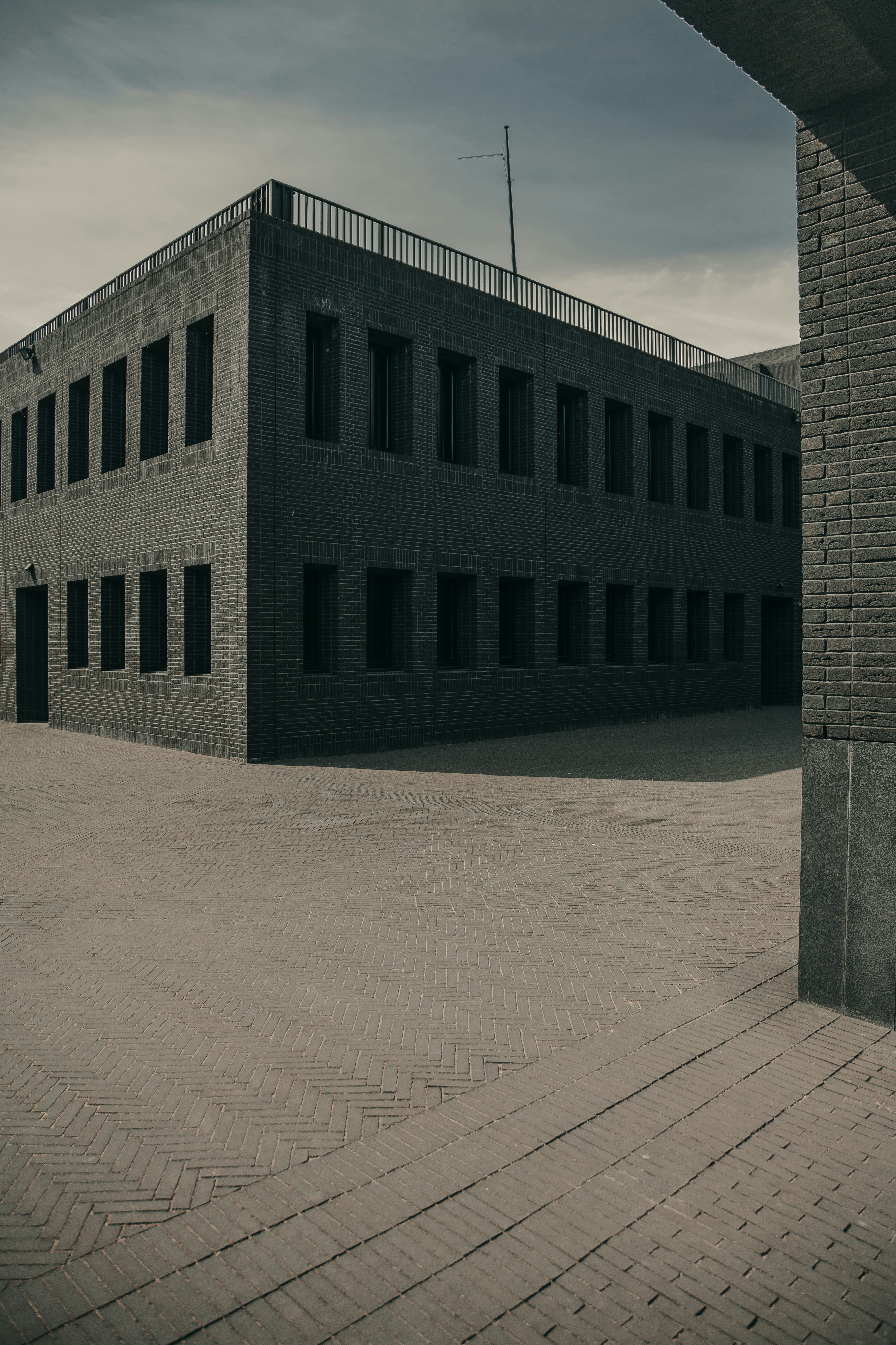 A minimalist architectural scene featuring a brick building with a stark interplay of light and shadow, emphasizing its geometric forms and textures.