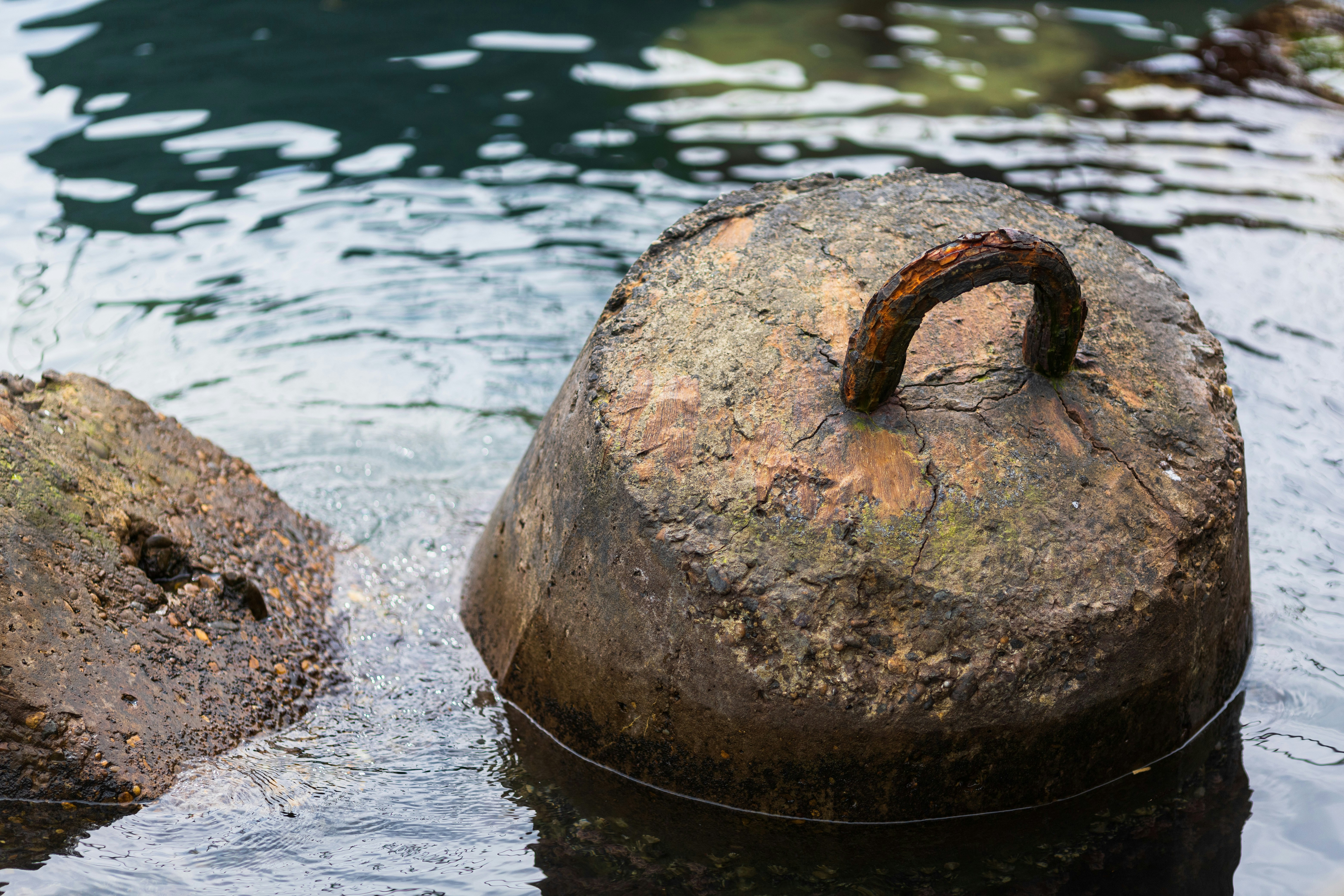 Weathered mooring anchor emerging from calm harbor water