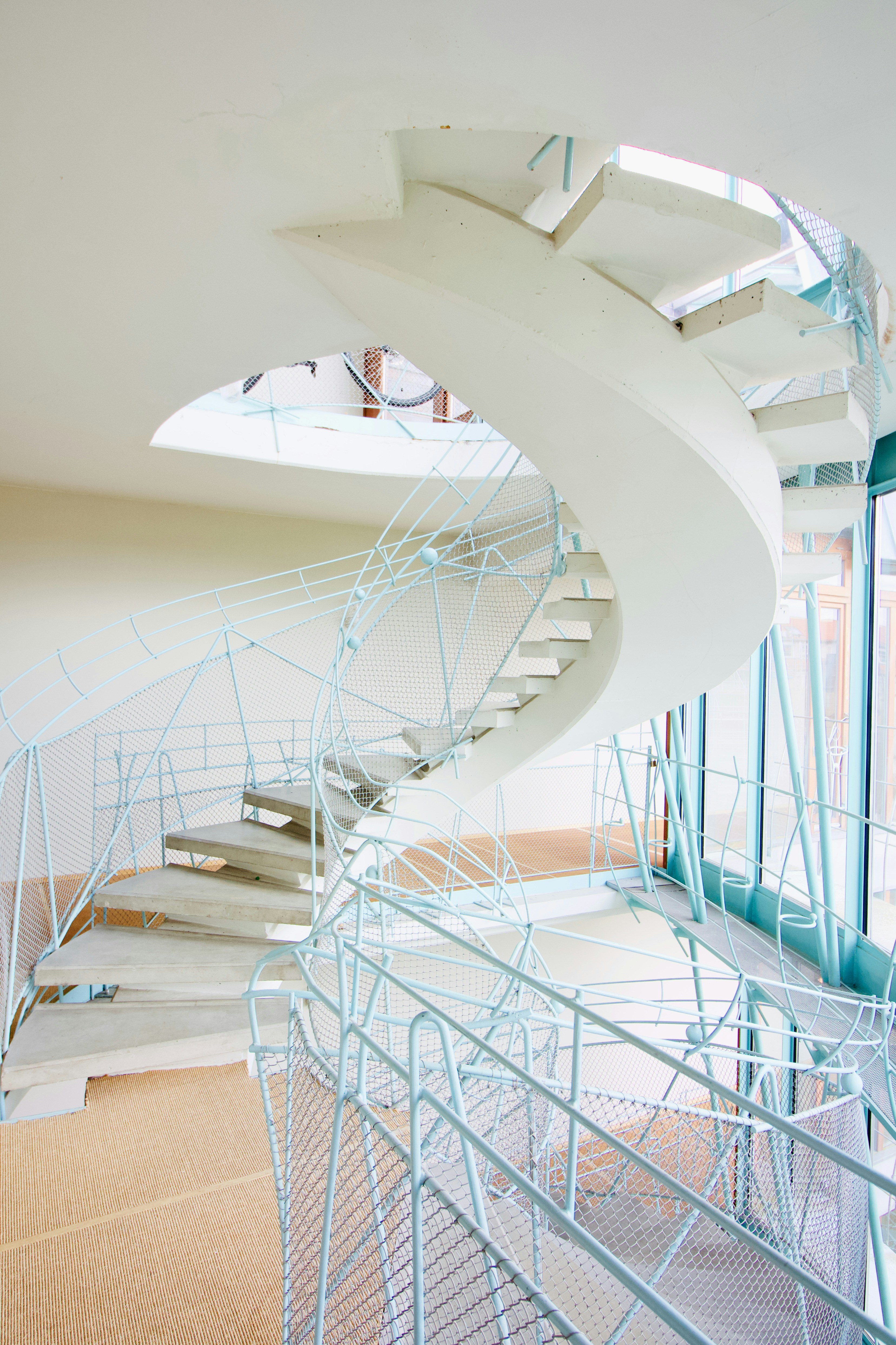 Innovative spiral staircase with delicate blue mesh and concrete steps, showcasing modern architectural design.