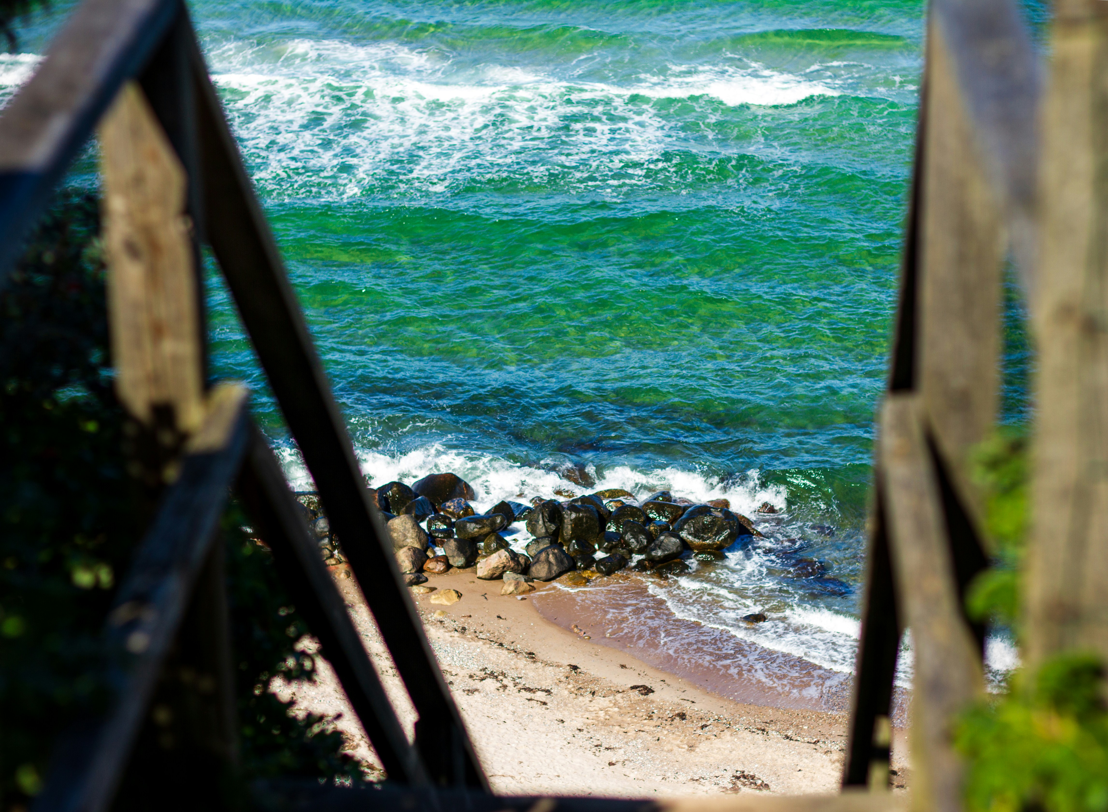 View of a rocky shoreline framed by wooden railings, showcasing the vibrant green waters and gentle waves lapping at the beach.
