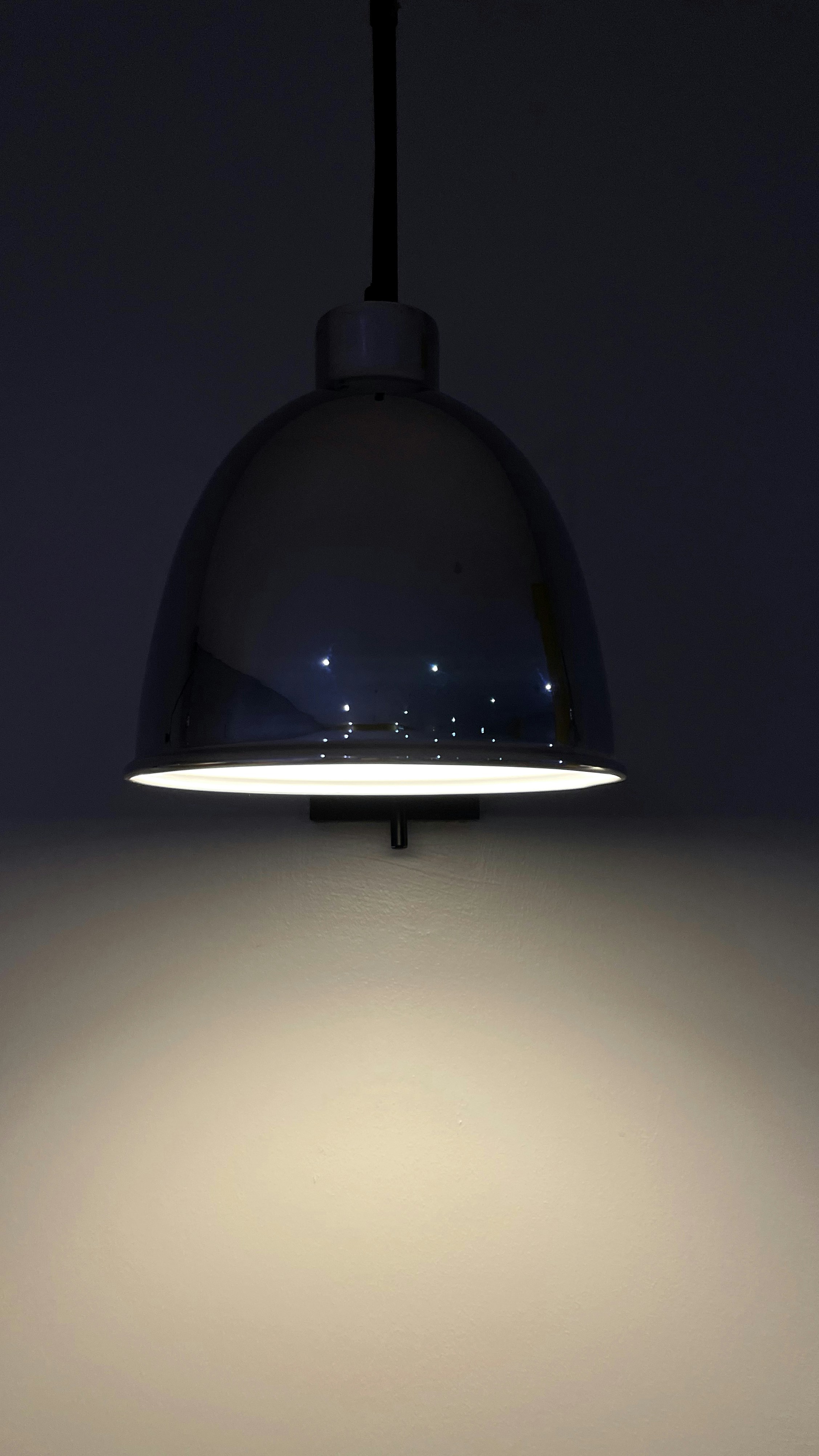 Sleek metallic pendant light casting a soft glow on a textured wall, enhancing the ambiance of the space.