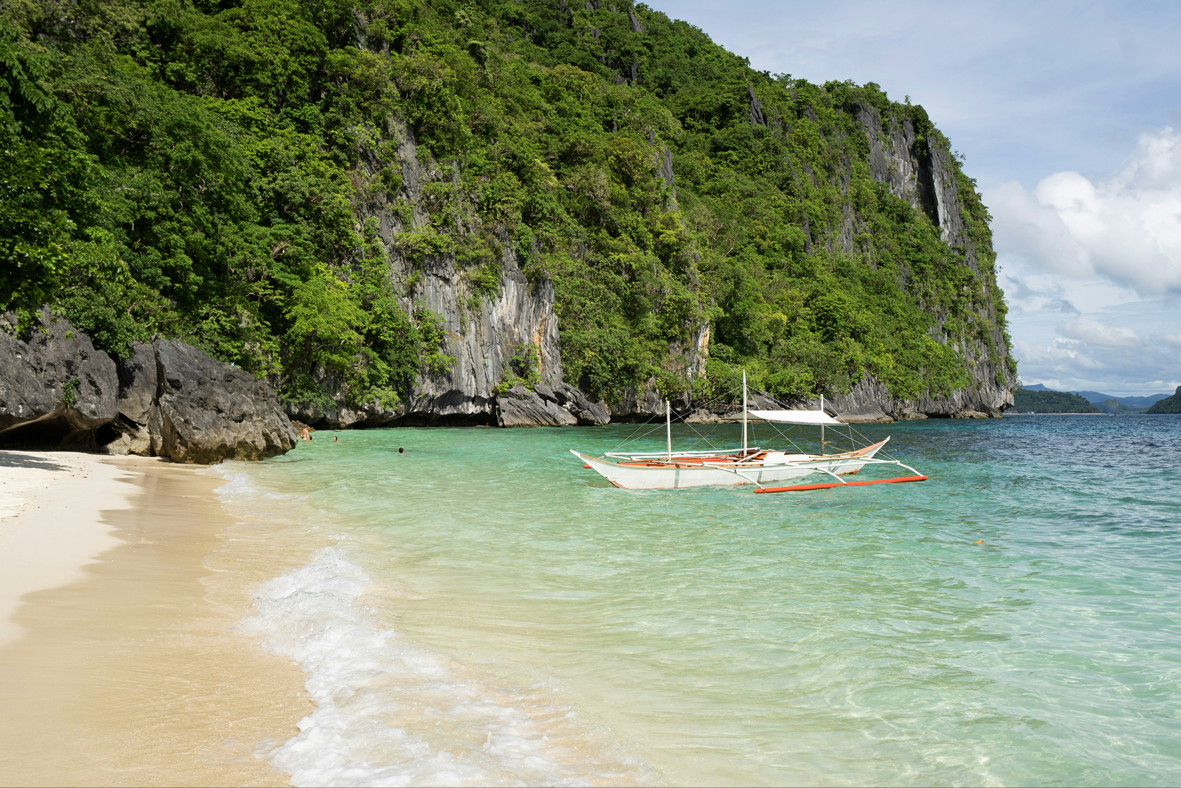 Spectacular beach view in El Nido, Palawan, Philippines. | white and red boat on sea near green mountain during daytime