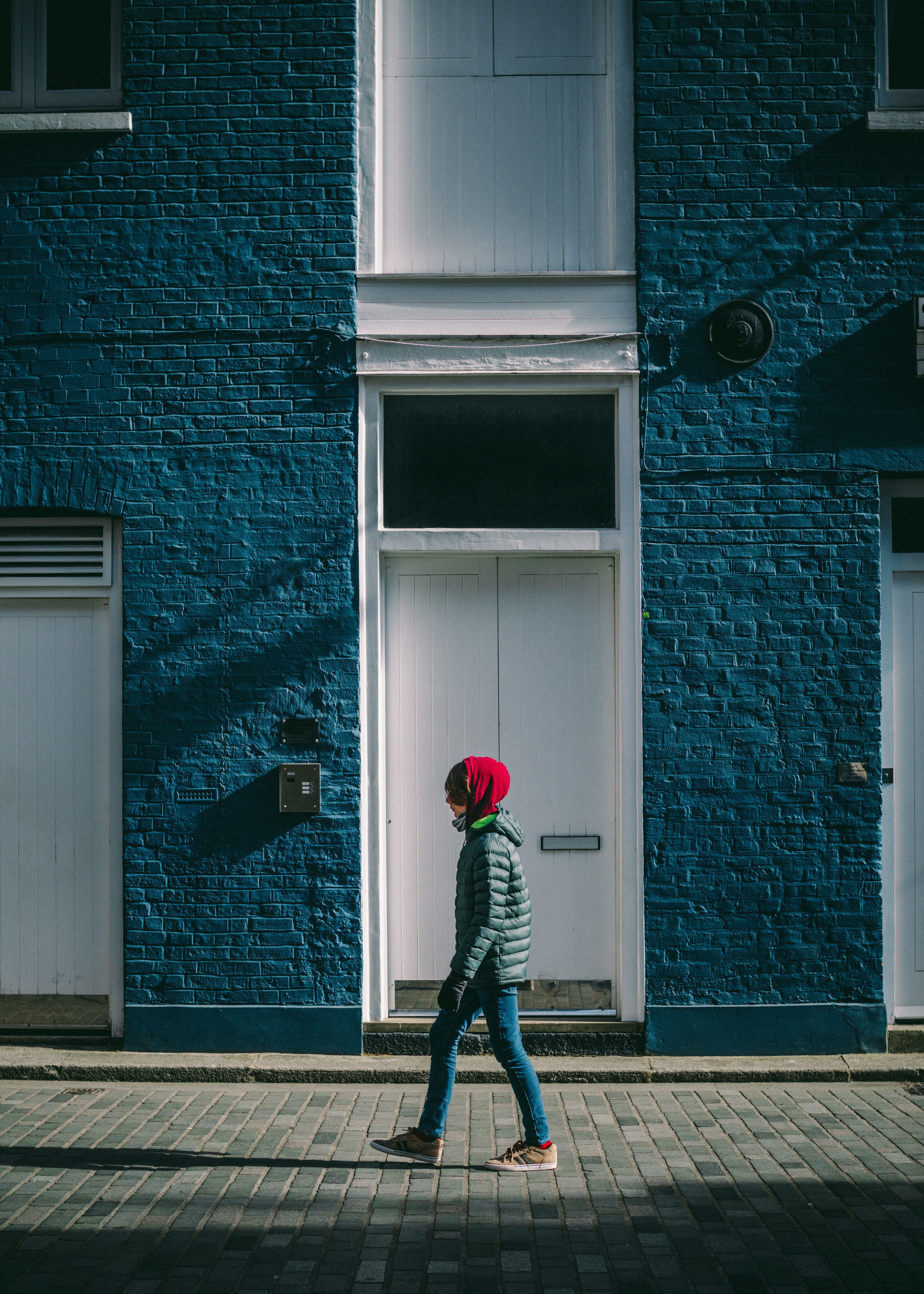 Red-Hooded Pedestrian Against a Cobalt Brick Facade