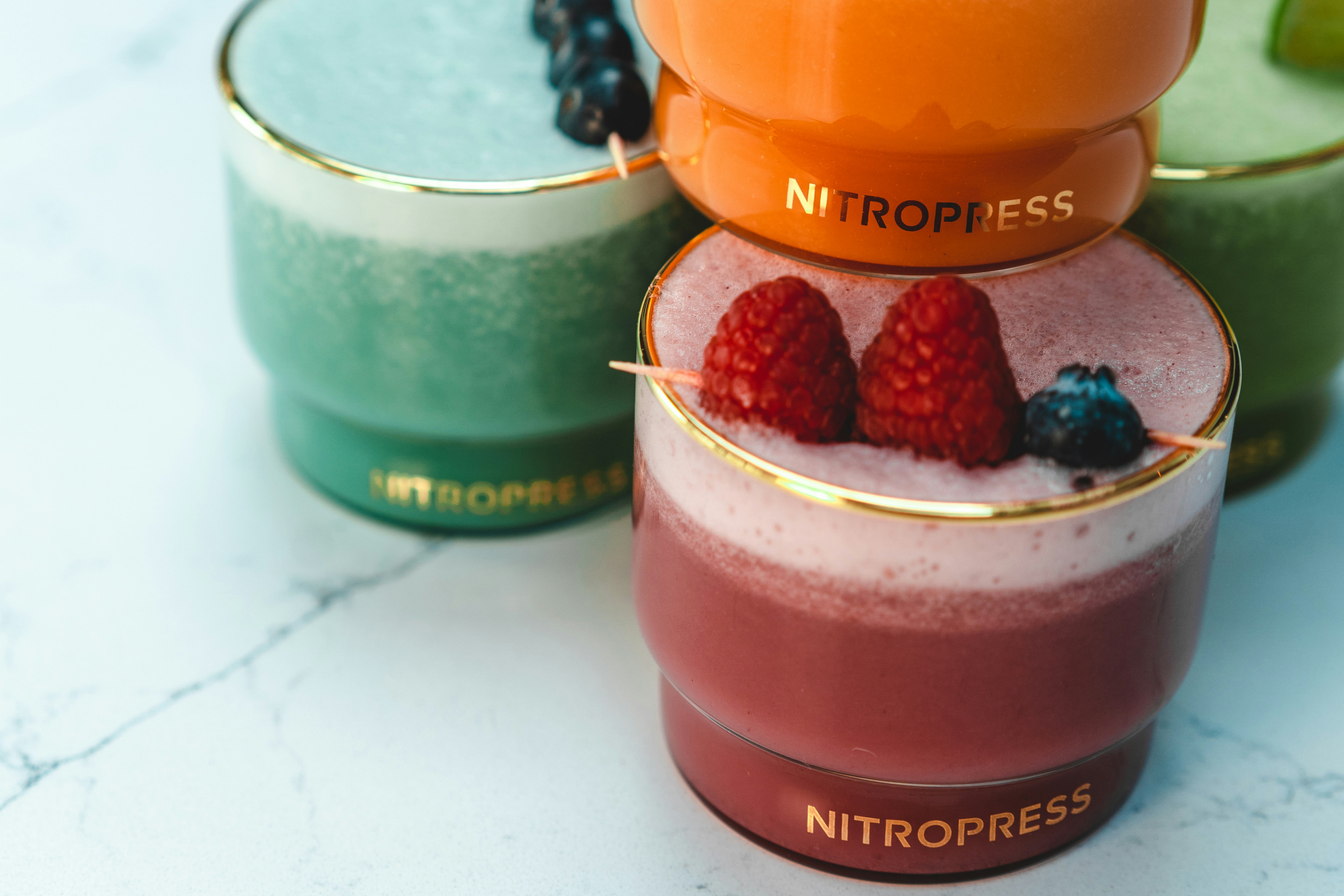 Colorful dessert cups filled with frothy layers and topped with fresh berries, arranged artistically on a marble surface.