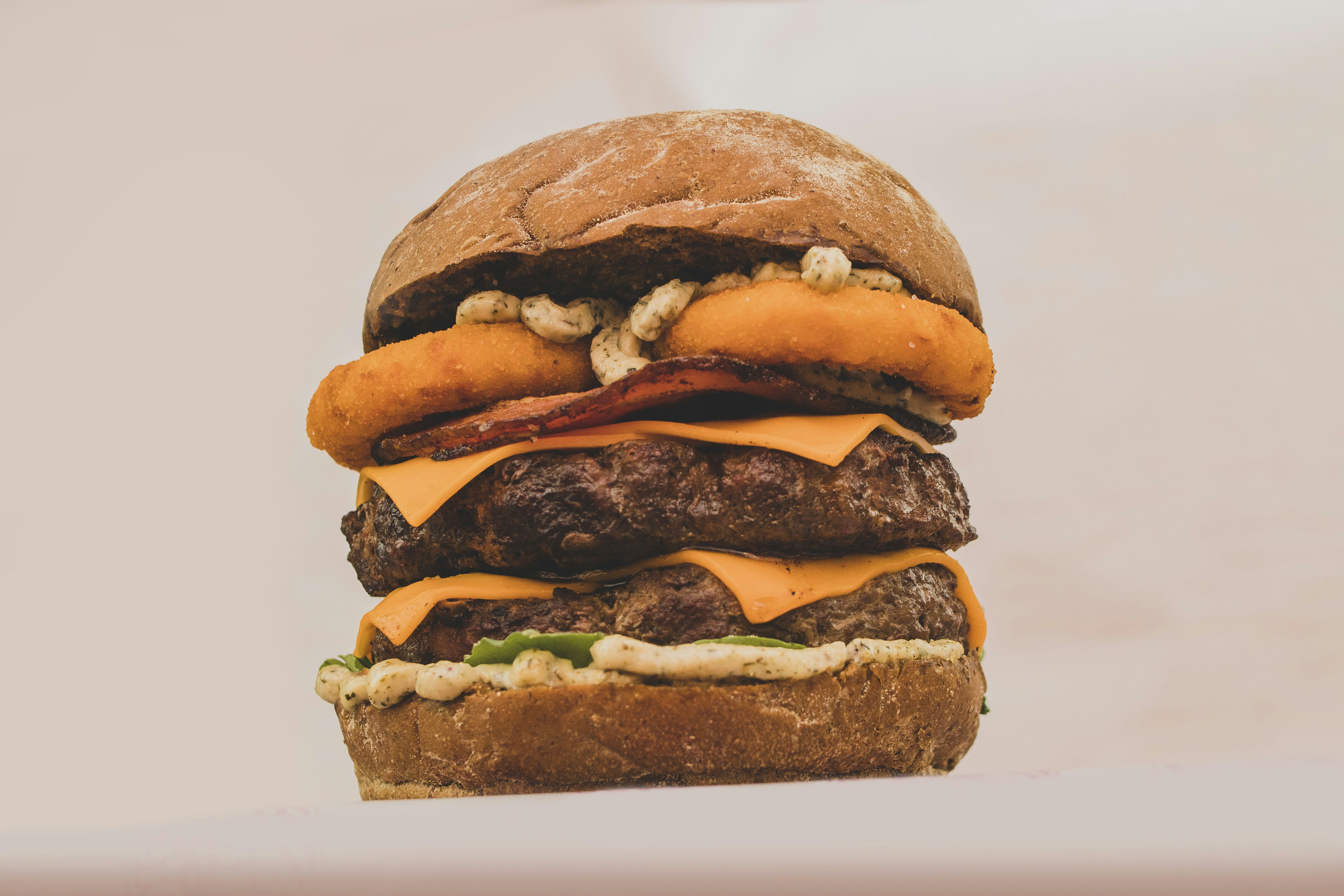 A towering burger featuring two juicy beef patties, melted cheese, crispy onion rings, and fresh lettuce, all nestled in a rustic bun.