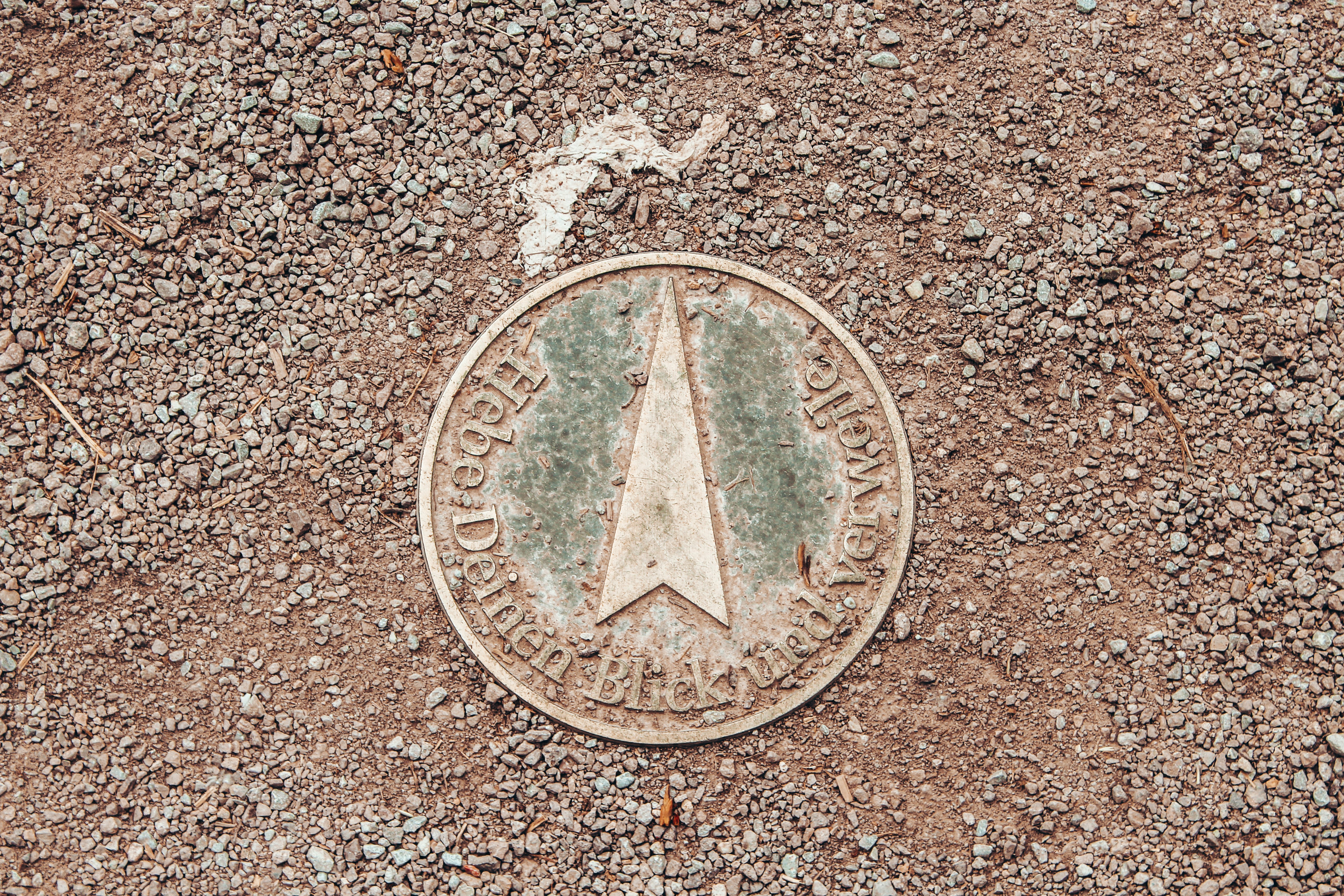 A weathered directional marker set into the ground, showcasing its faded details amidst a gravel surface.