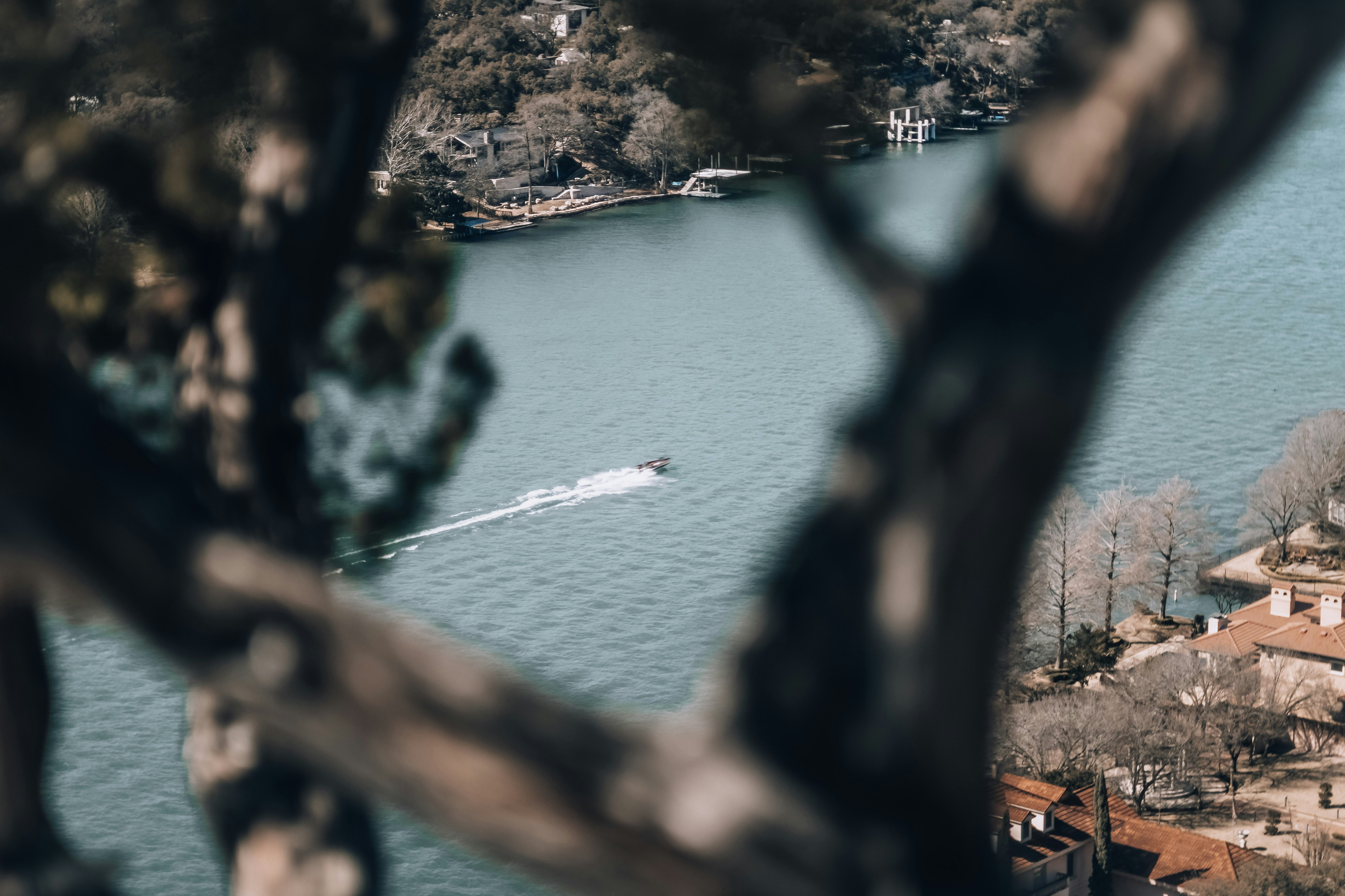 A boat glides across a tranquil river, framed by blurred tree branches, showcasing a peaceful outdoor scene.