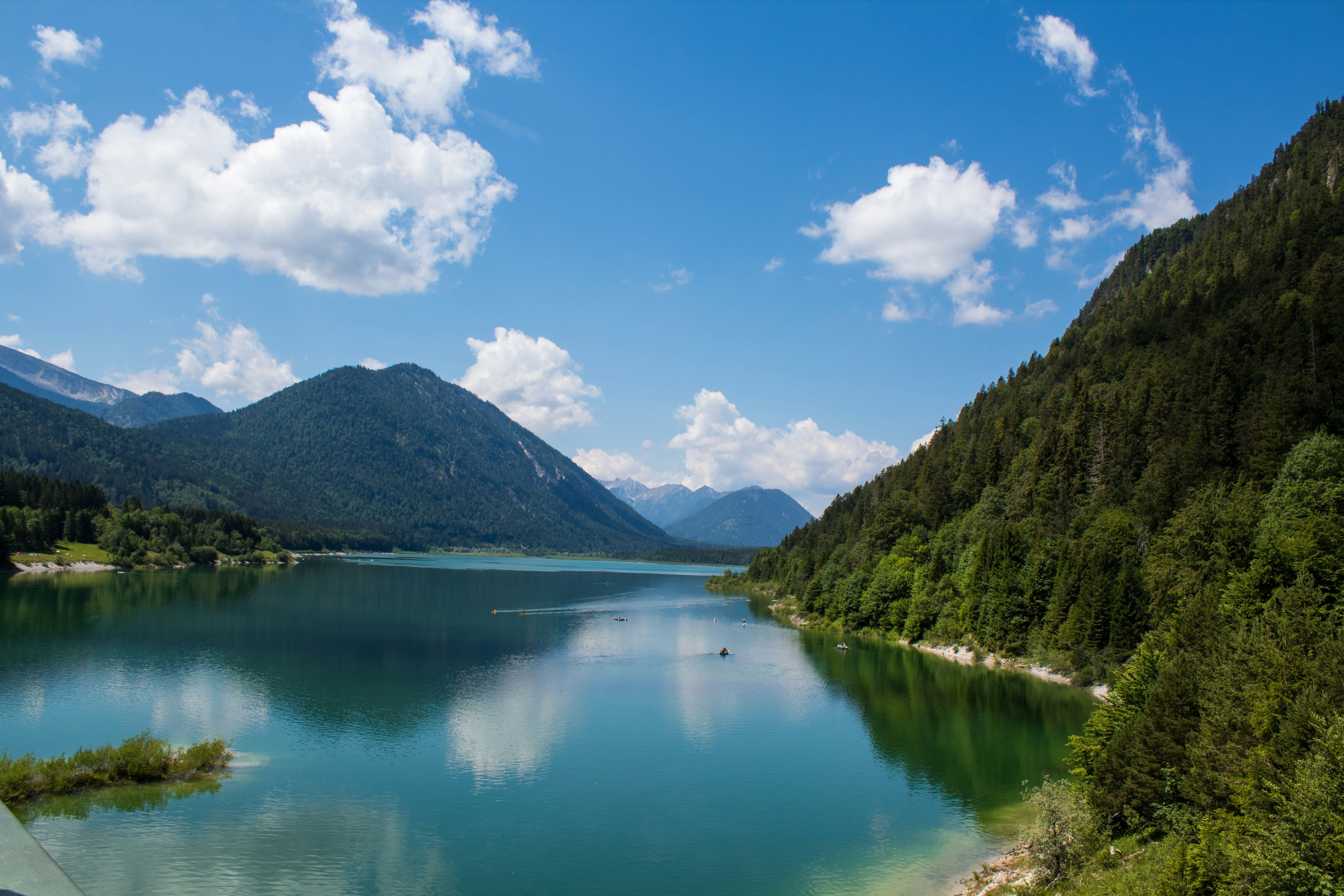 Serene lake reflecting lush green trees and majestic mountains under a vibrant blue sky.