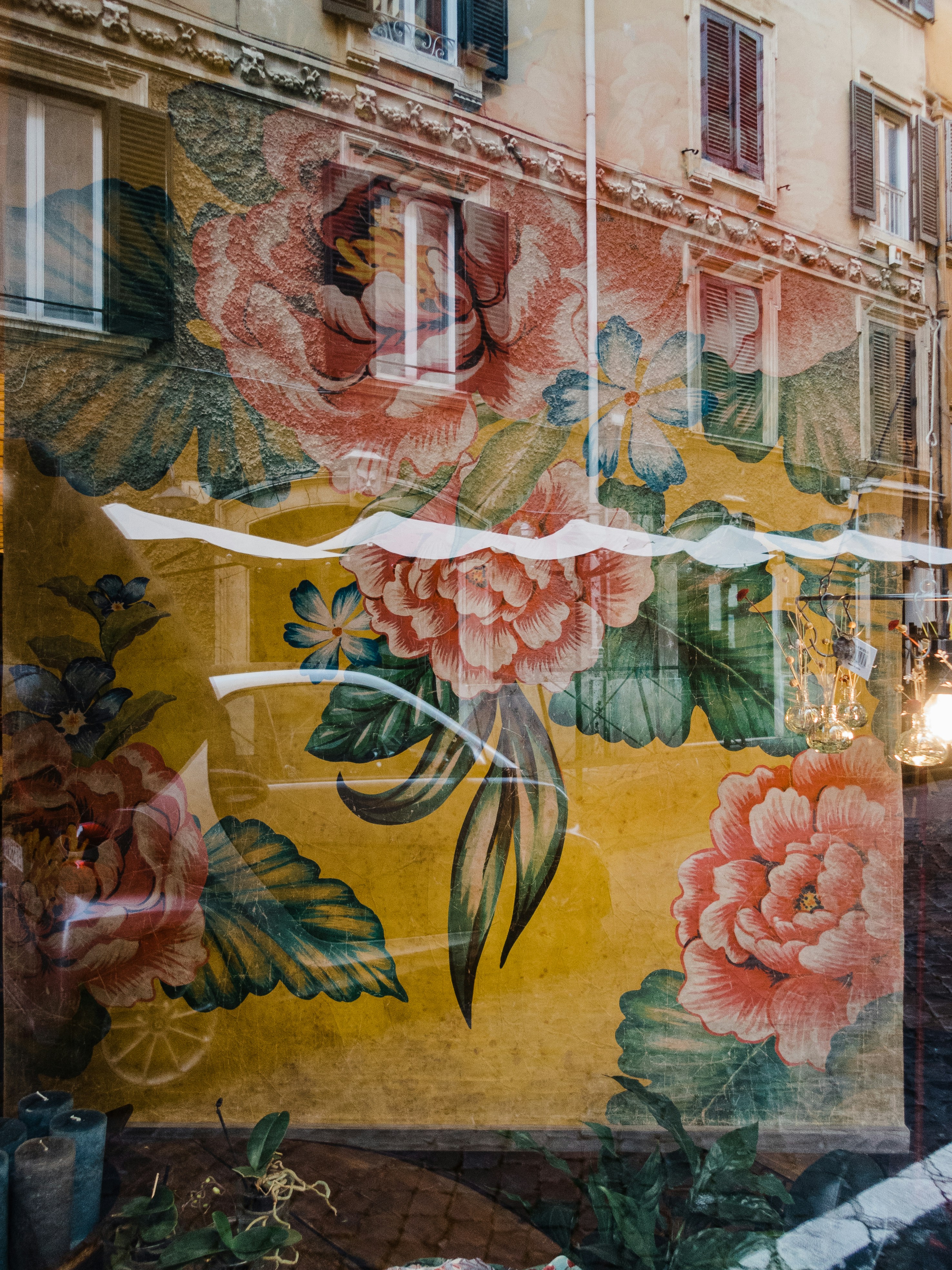 Vibrant floral mural reflecting in a shop window, showcasing intricate details against a warm yellow backdrop.