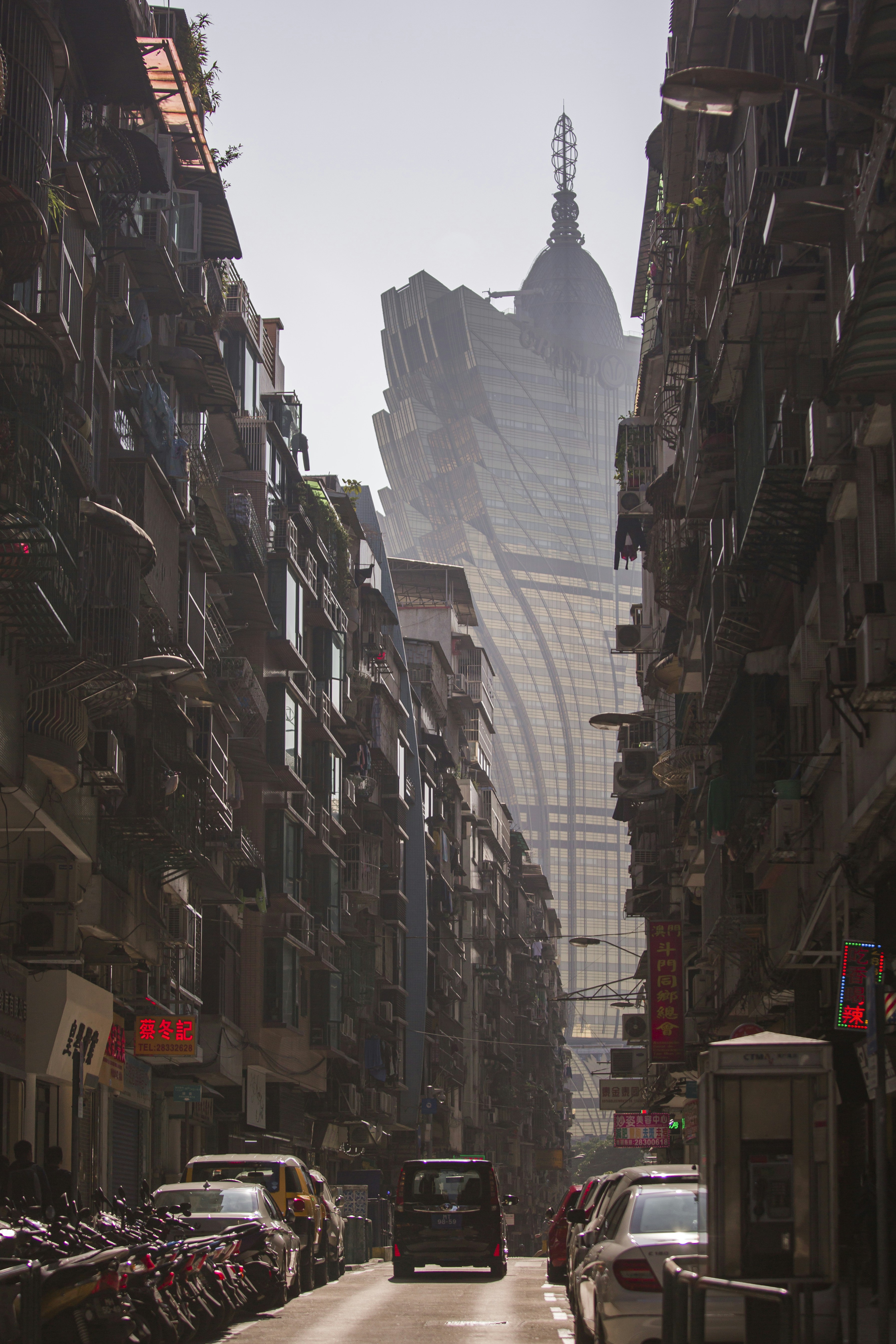 Narrow street flanked by historic buildings with a modern skyscraper looming in the background. The scene captures the juxtaposition of old and new architecture.