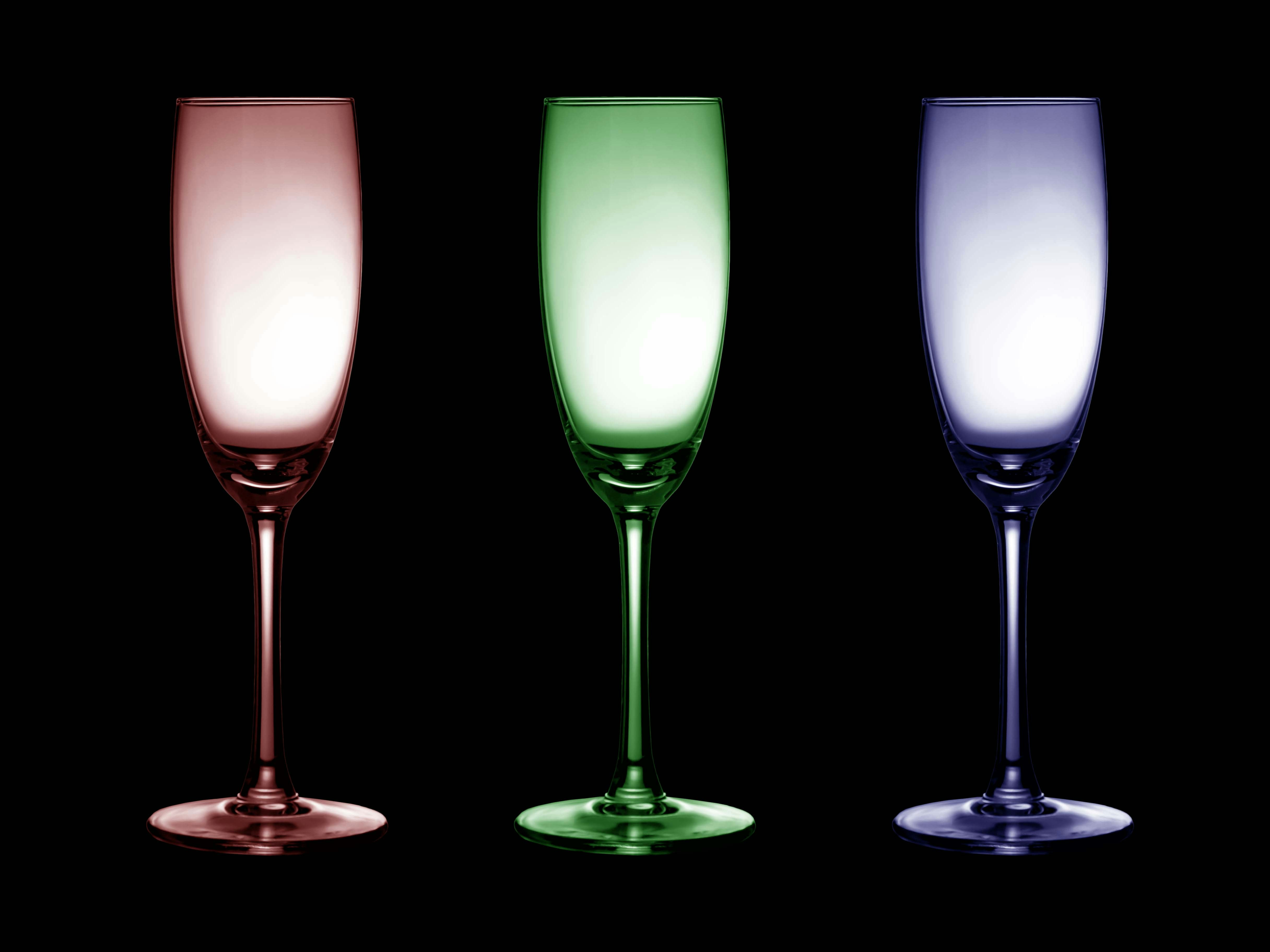 Three elegant champagne flutes in shades of red, green, and blue, illuminated against a dark backdrop, showcasing their vibrant hues and delicate shapes.