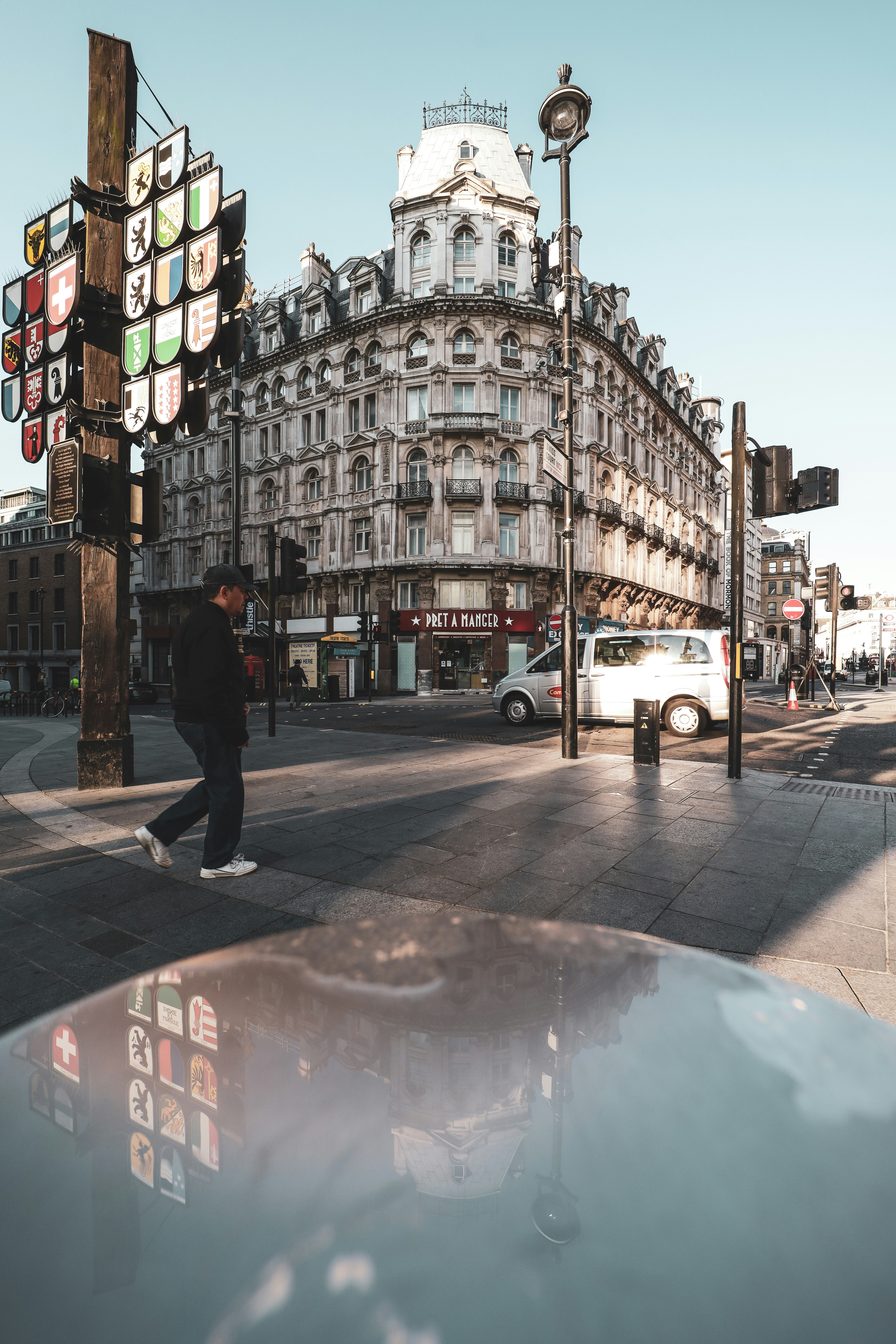 Man walking past a historic building with European crests and reflections in a cityscape during daytime.