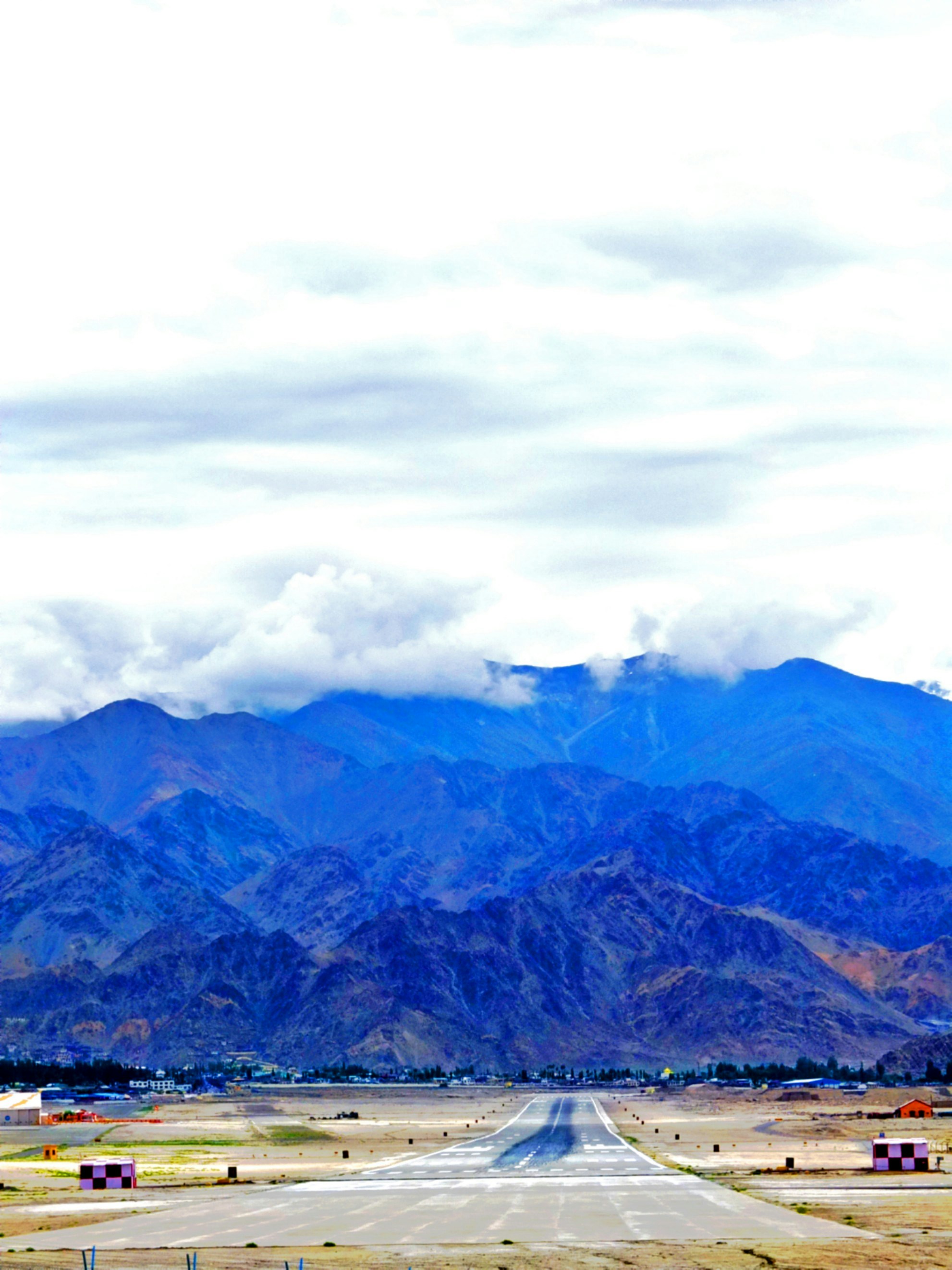 Aerial view of a runway leading toward majestic mountains under a cloudy sky. The scene captures the essence of travel and exploration.