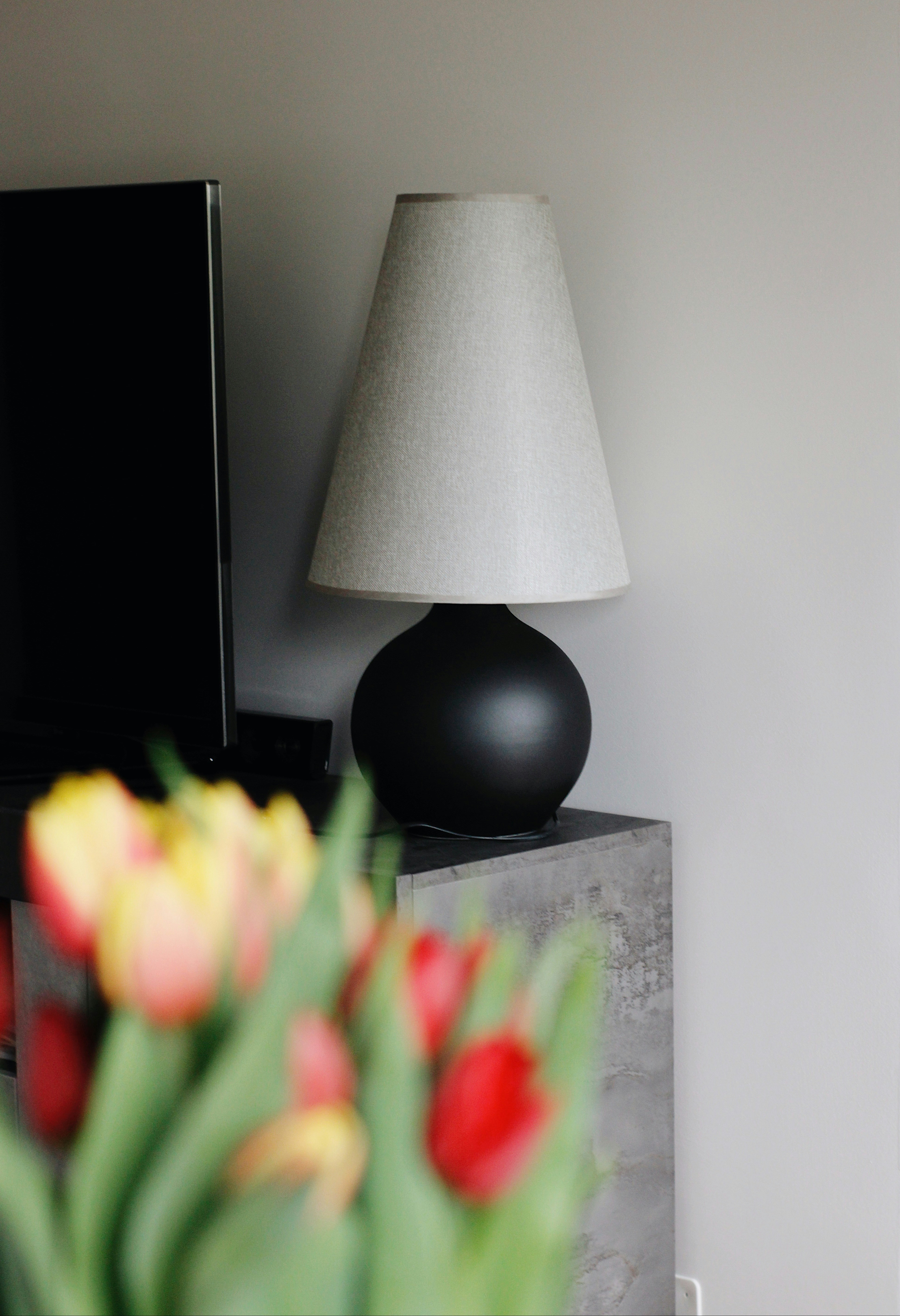 Shade and Sphere: A Quiet Lamp Anchored on Concrete with Foreground Tulips