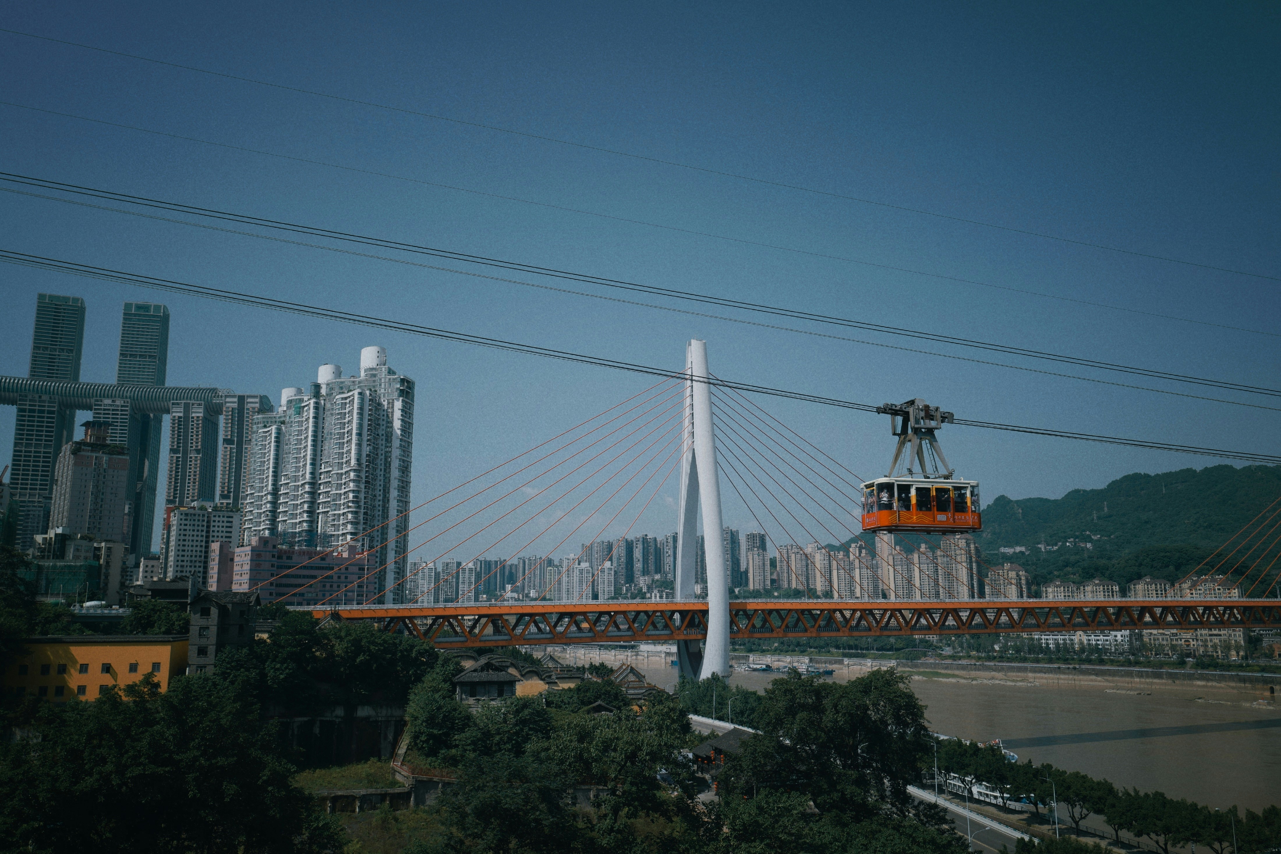 Orange Gondola Crossing the White Pylon: A Cable-Stayed Bridge Framing a River City