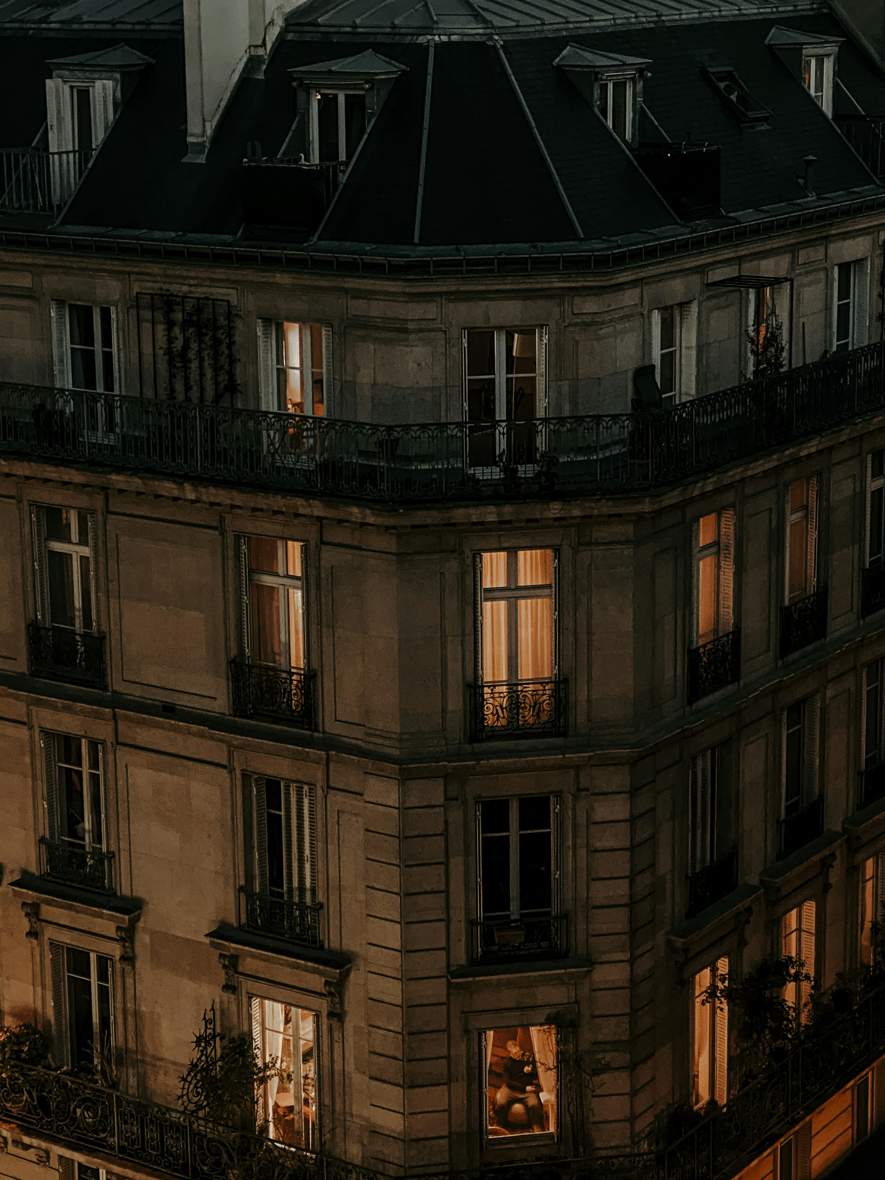 Illuminated windows of a Parisian building reveal glimpses of life within as night falls. The intricate architecture showcases the charm of the city.