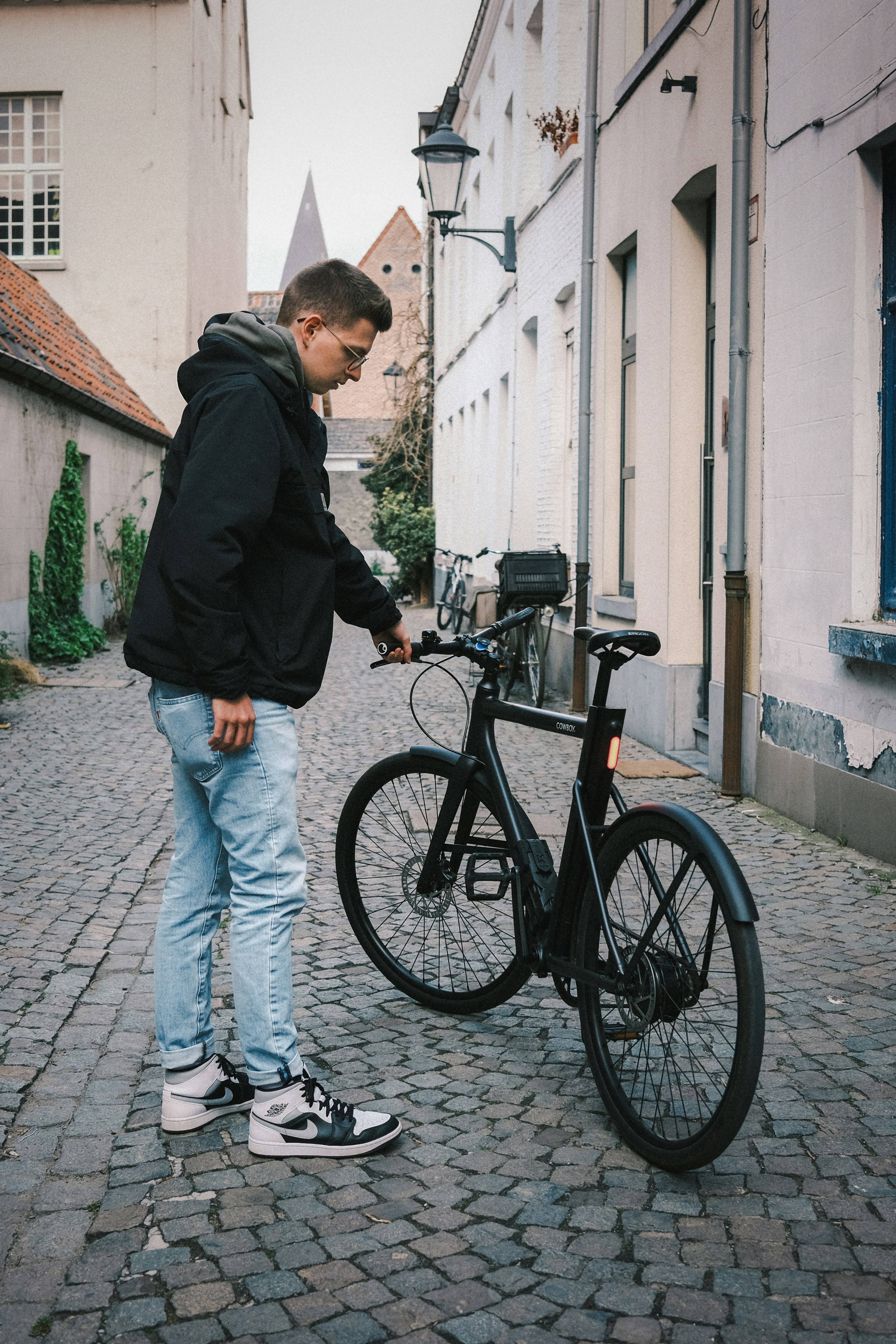 Cobbled Quiet: A Man Tends to a Black E-Bike in a Narrow European Alley
