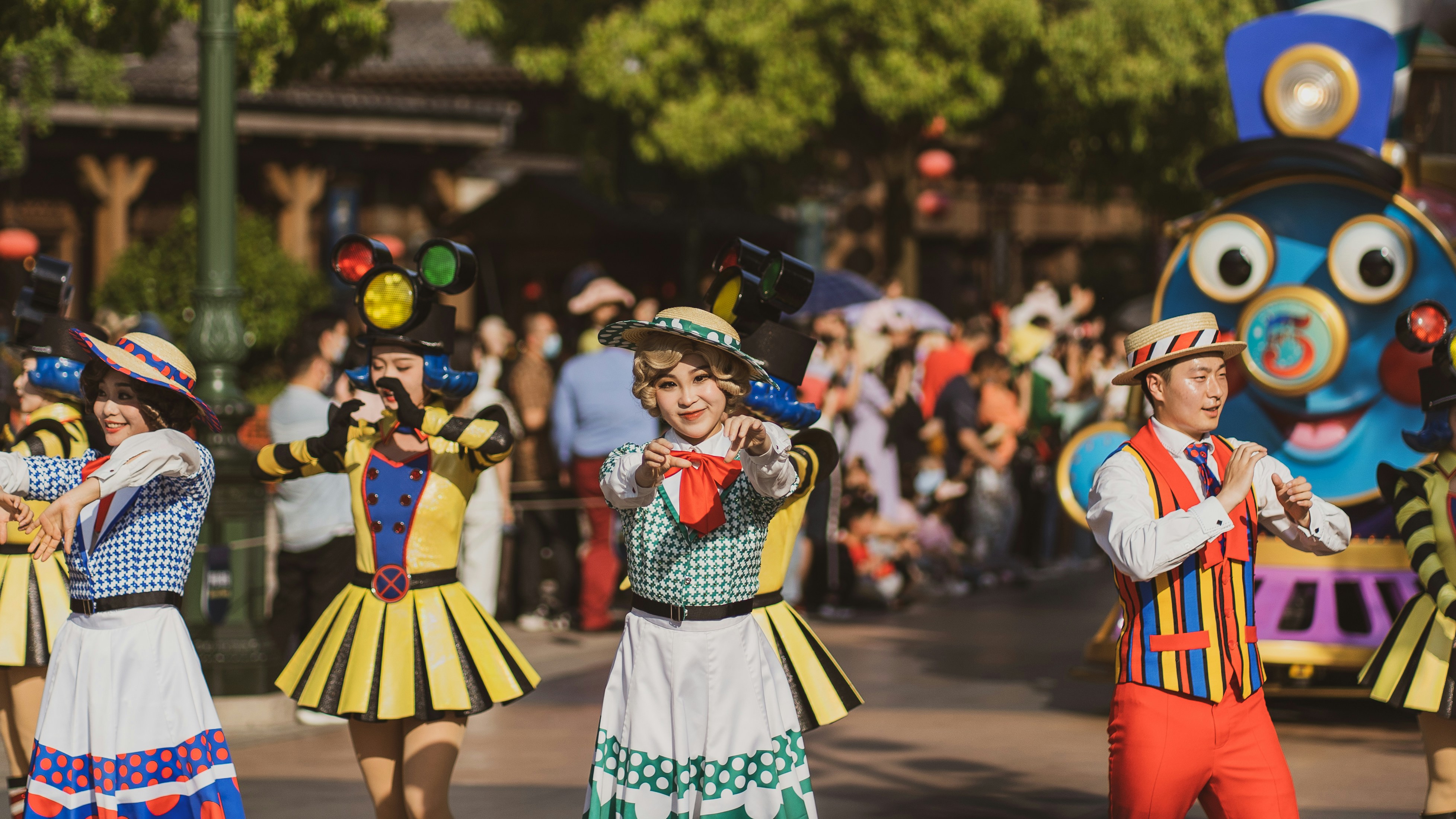 Colorful performers in vintage costumes engage an audience during a lively parade, with a whimsical train in the background.