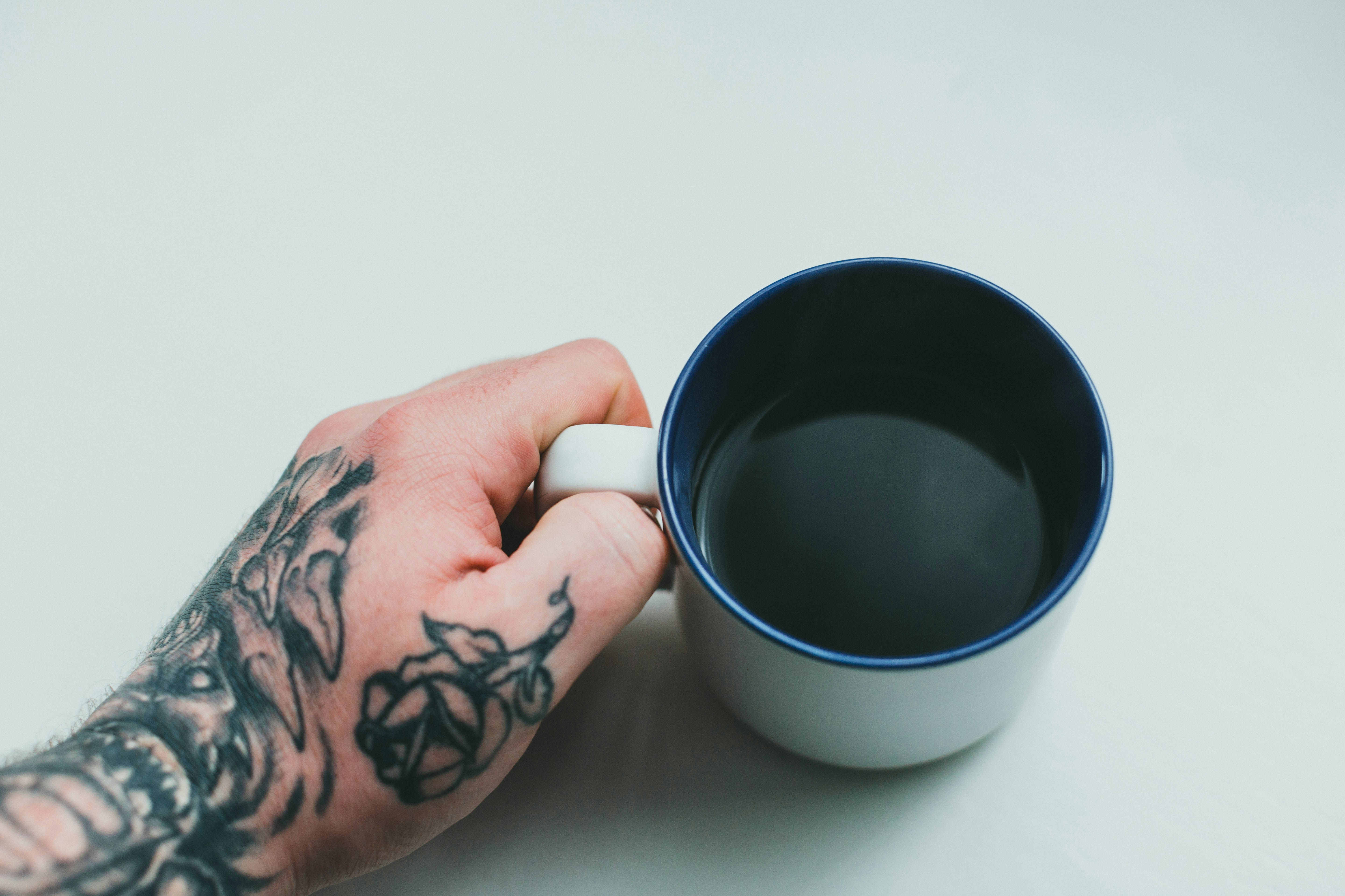 Ink and Porcelain: A Tattooed Hand Clutches a Mug in Soft Light