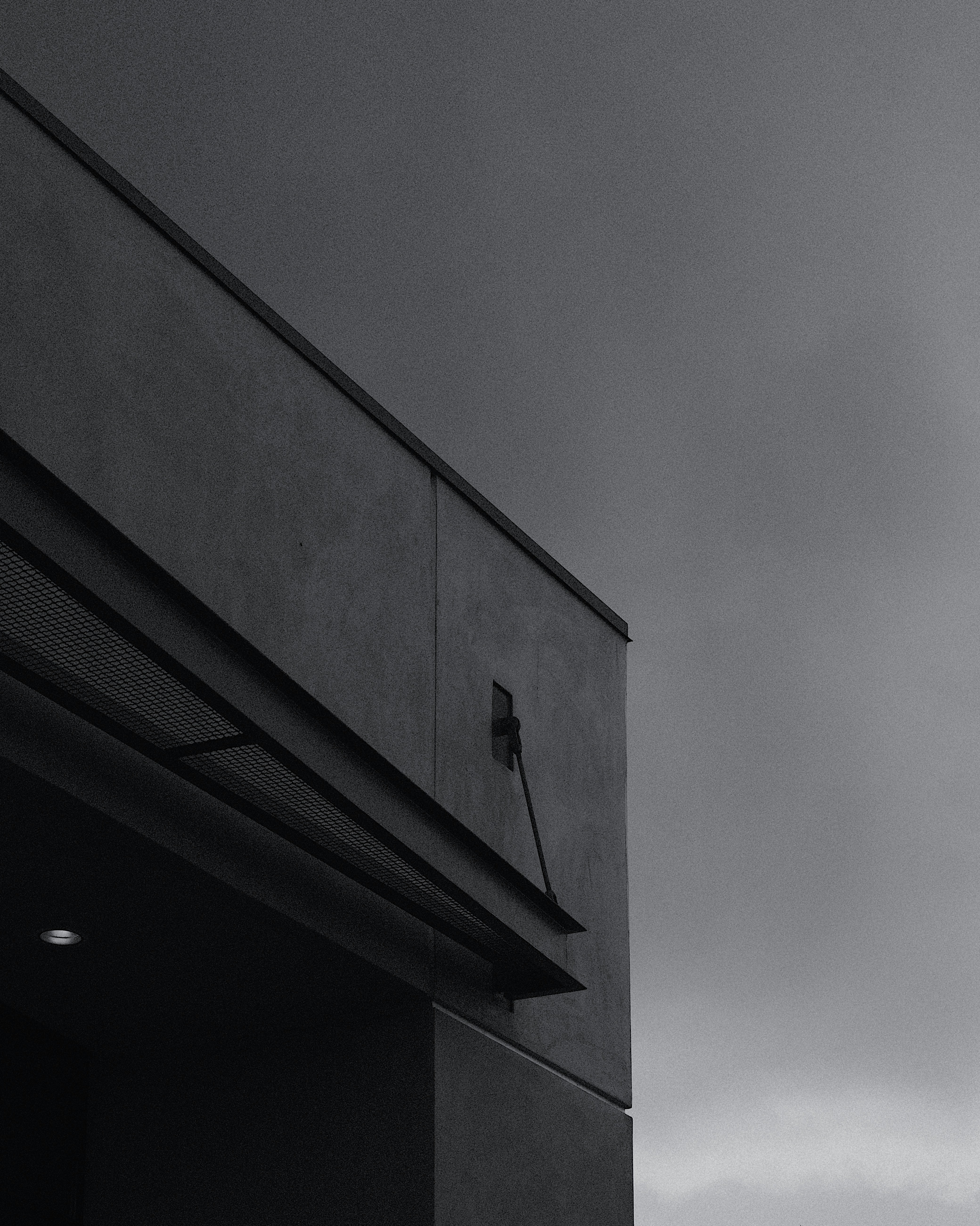 Minimalist building corner under a cloudy sky, emphasizing geometric lines and textures. The interplay of light and shadow creates a dramatic effect.