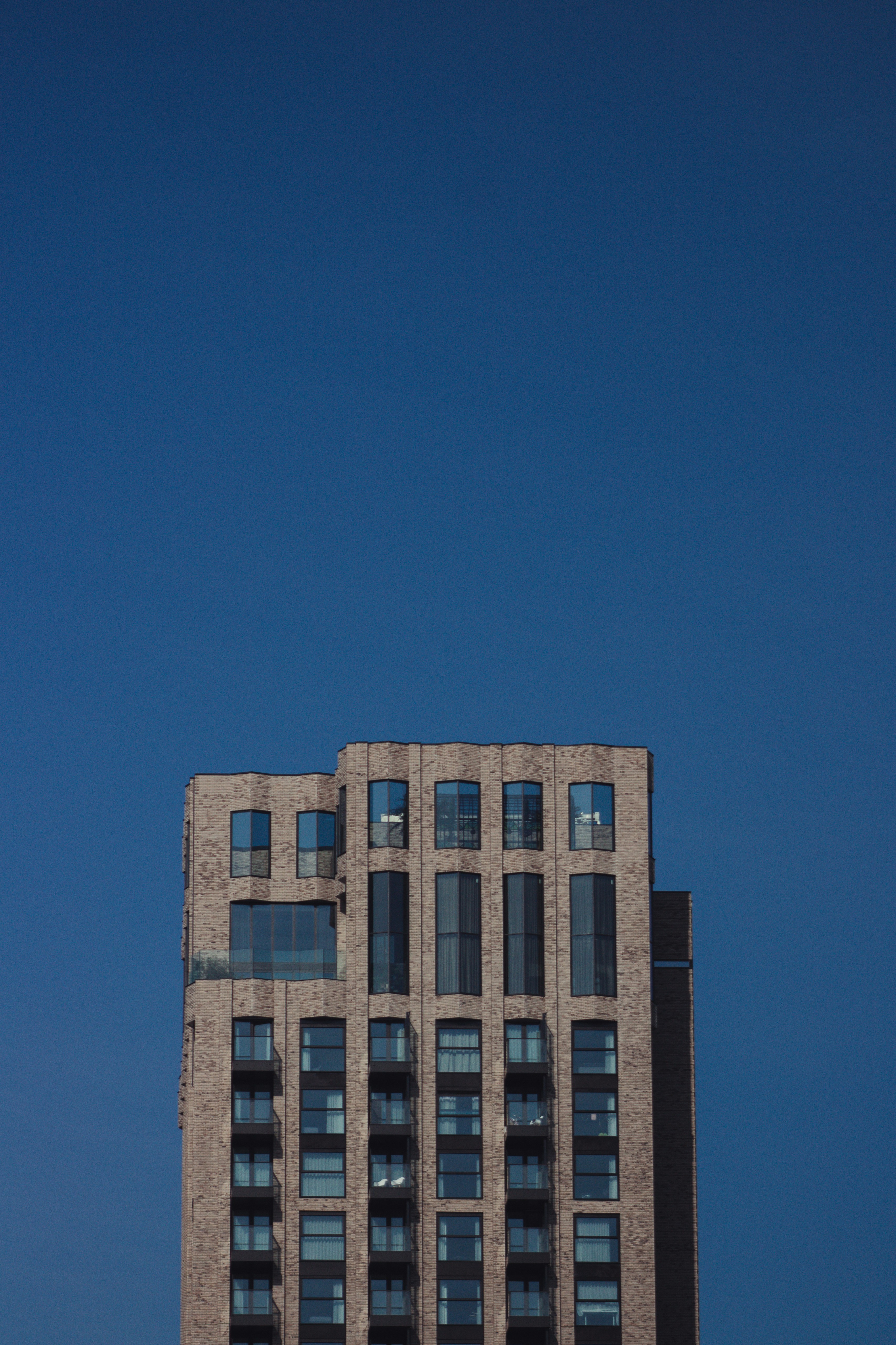Modern brick high-rise building with distinct window arrangements set against a bright blue sky.