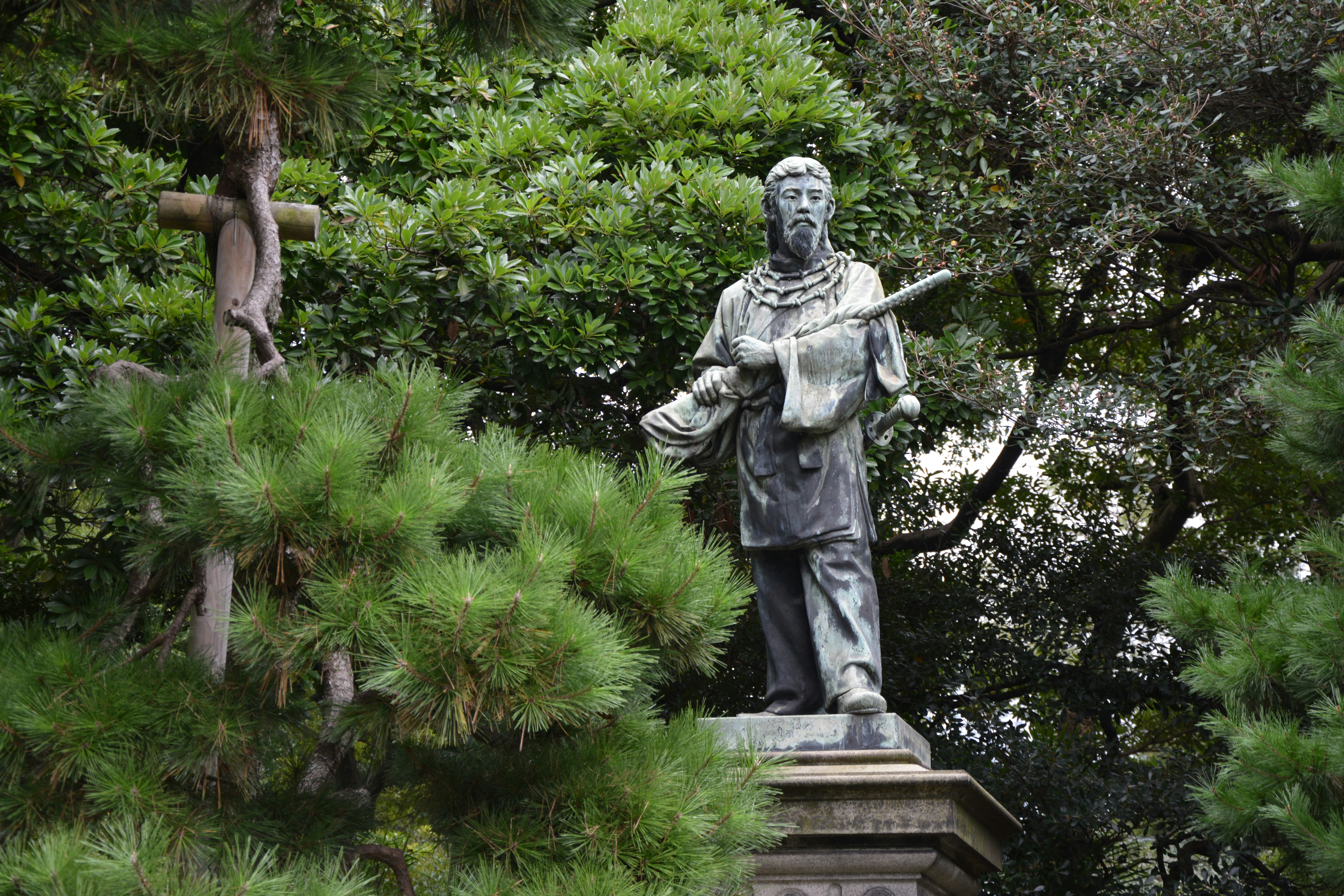 Statue in Green Quiet: A Scholar Stands Amid Pine Fronds