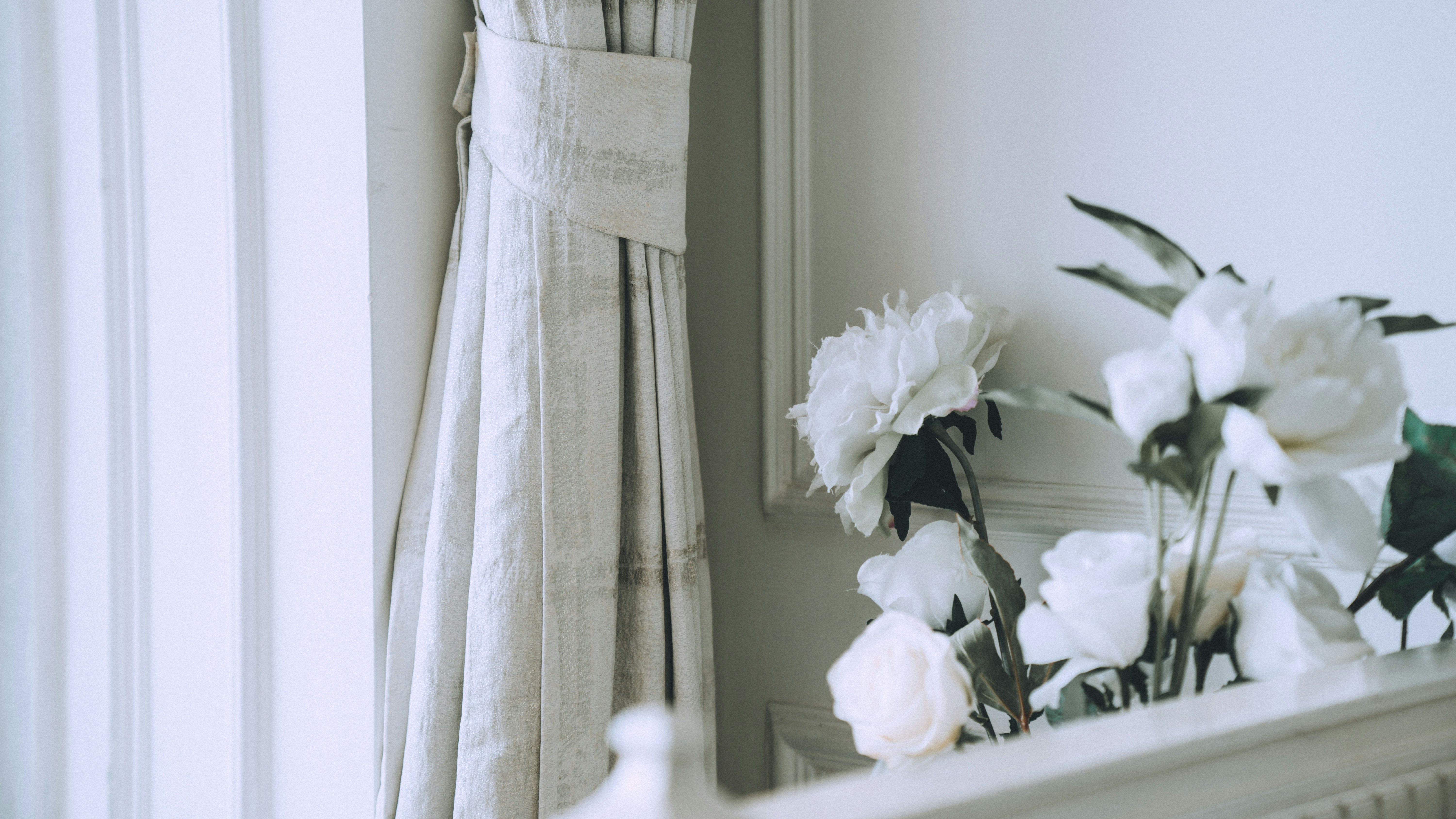 Delicate white flowers arranged beside a soft, textured curtain in a softly lit interior space.