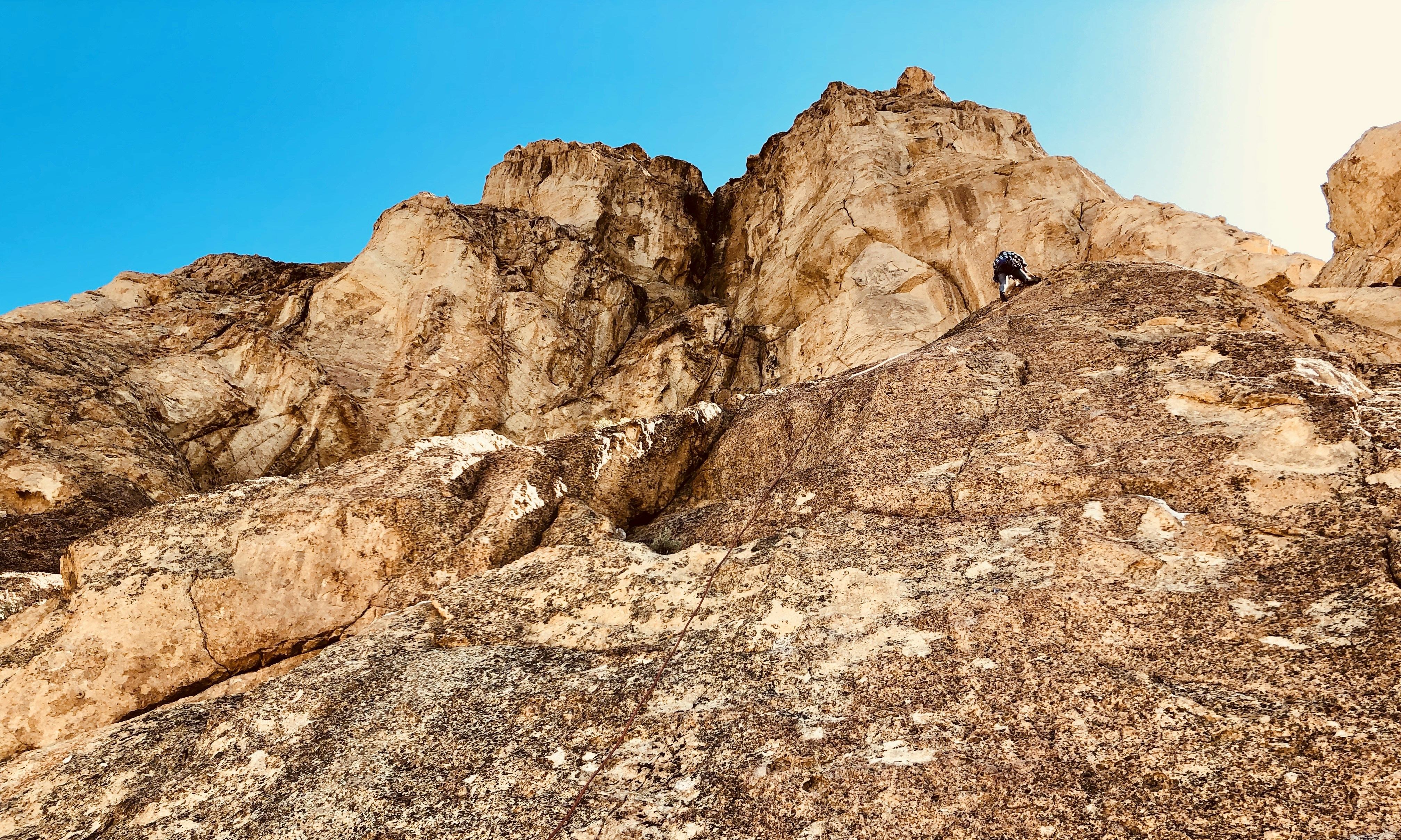 A climber scaling a rugged rock face under a clear blue sky, showcasing the thrill of outdoor adventure.