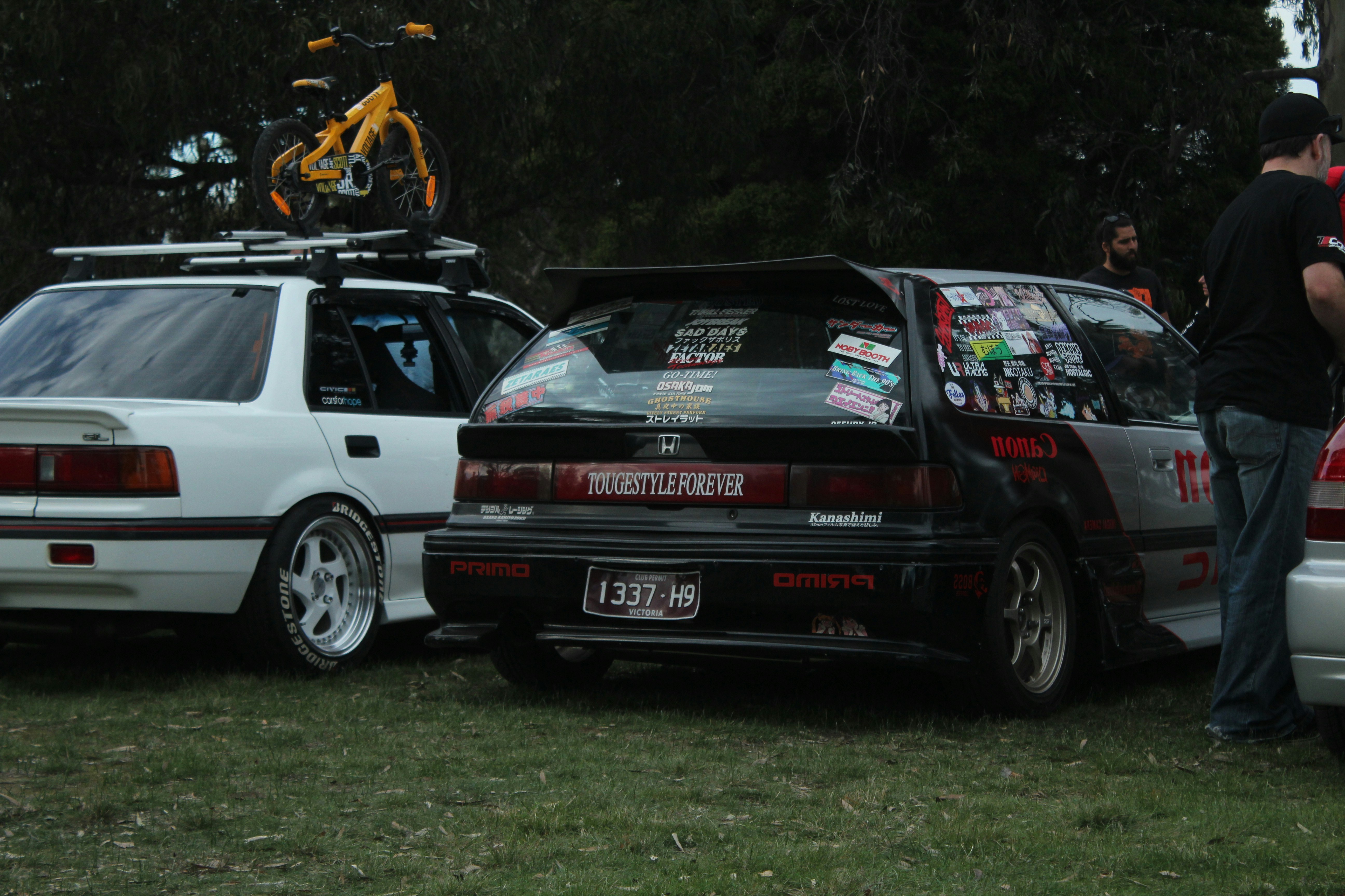 Dark-clad car with stickers and a roof bike in a casual car meet