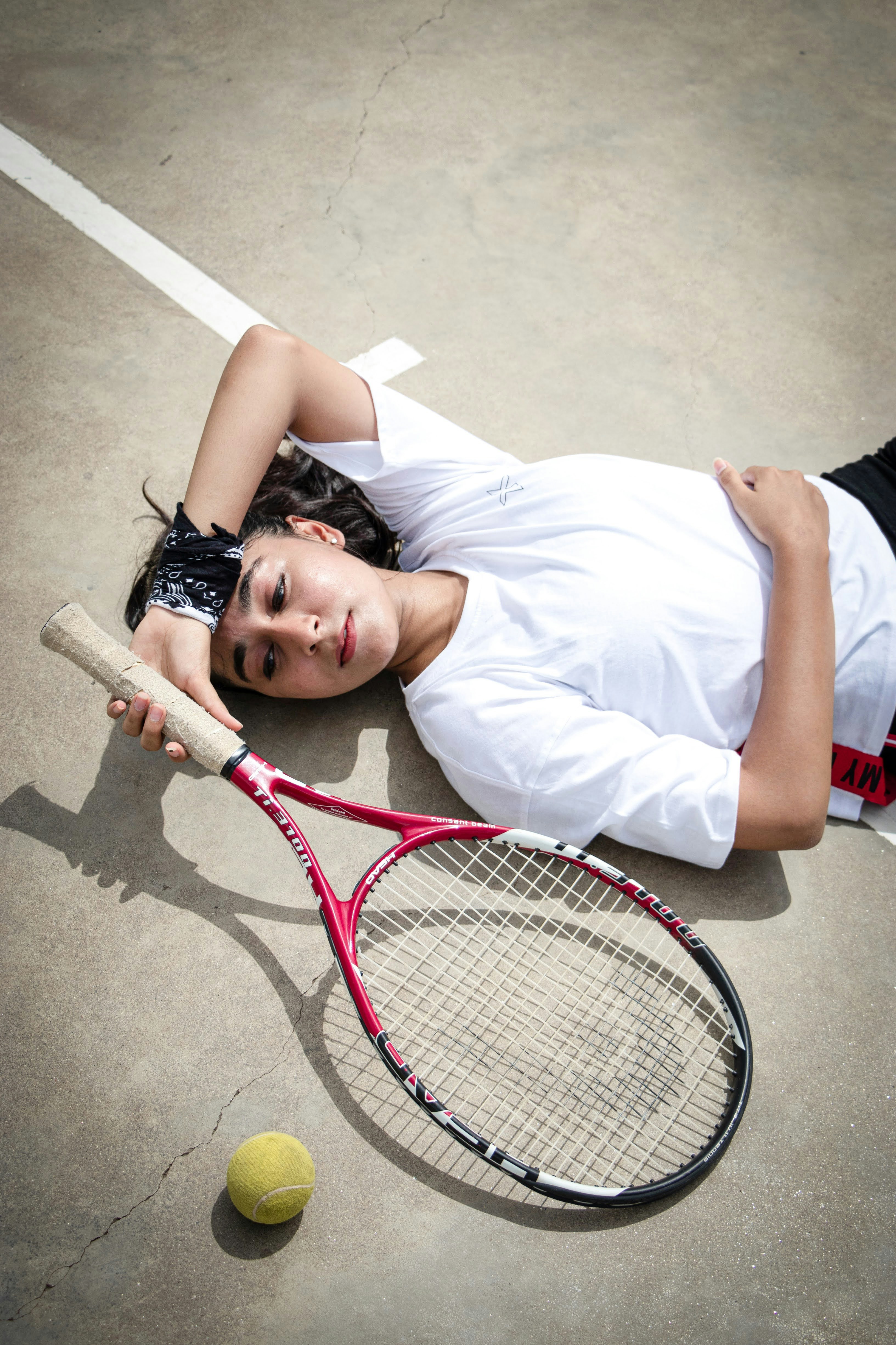 Athlete lying on the ground with a tennis racket and ball, capturing a moment of pause and contemplation.
