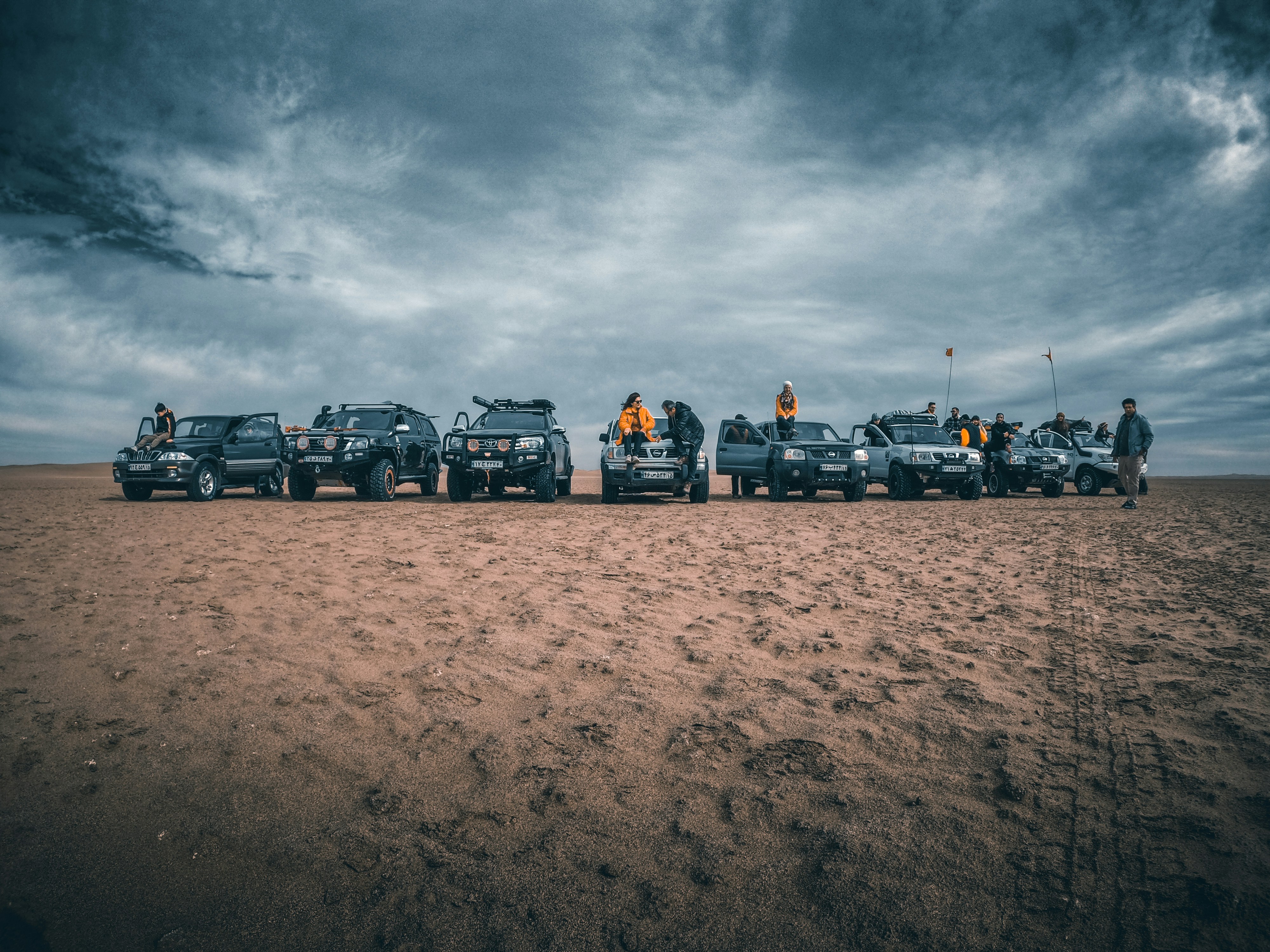 Lineup of rugged off-road vehicles on a sandy beach beneath a cloudy sky, ready for exploration.