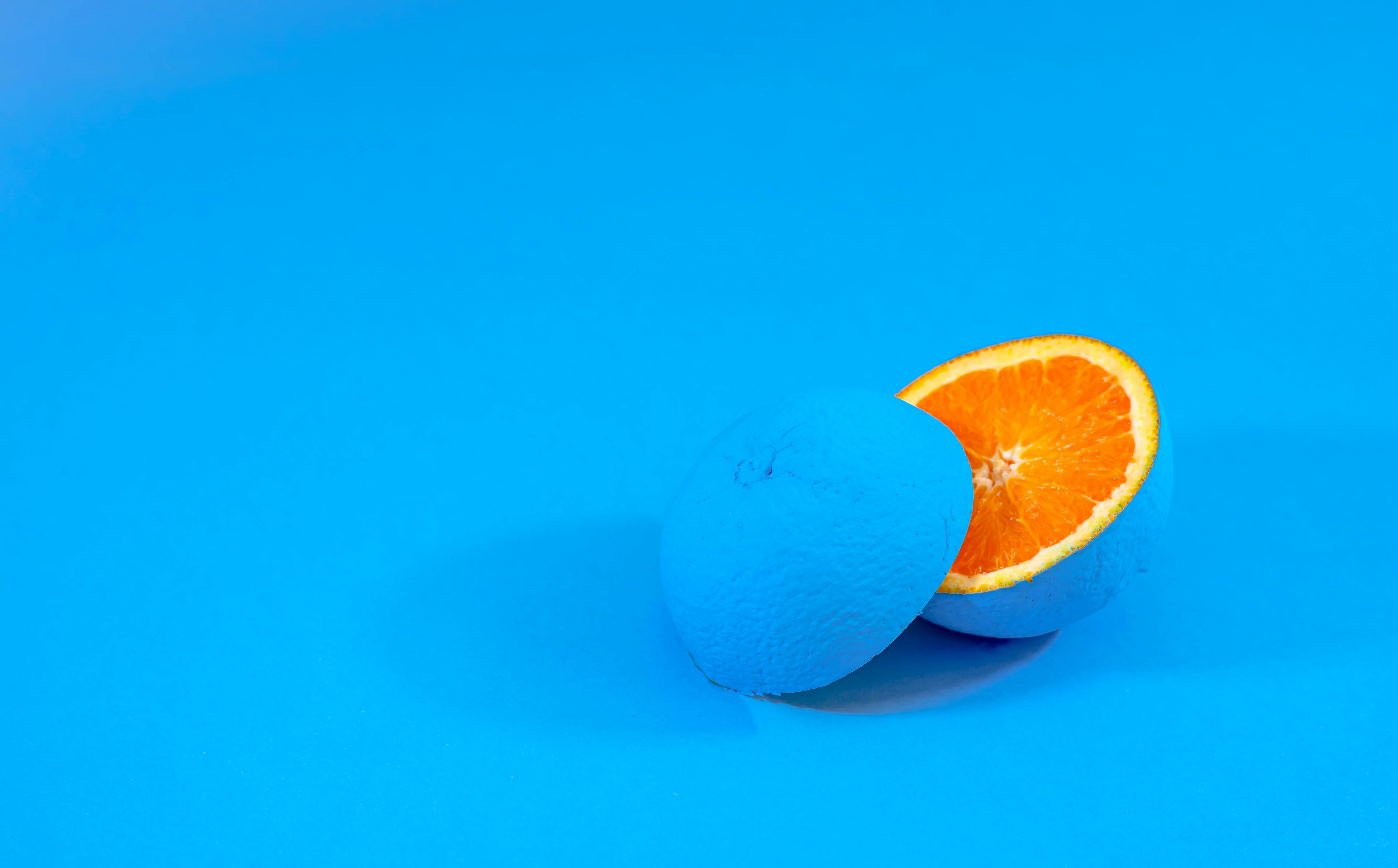 A bright blue spherical object cut in half, revealing a juicy orange interior against a solid blue background.