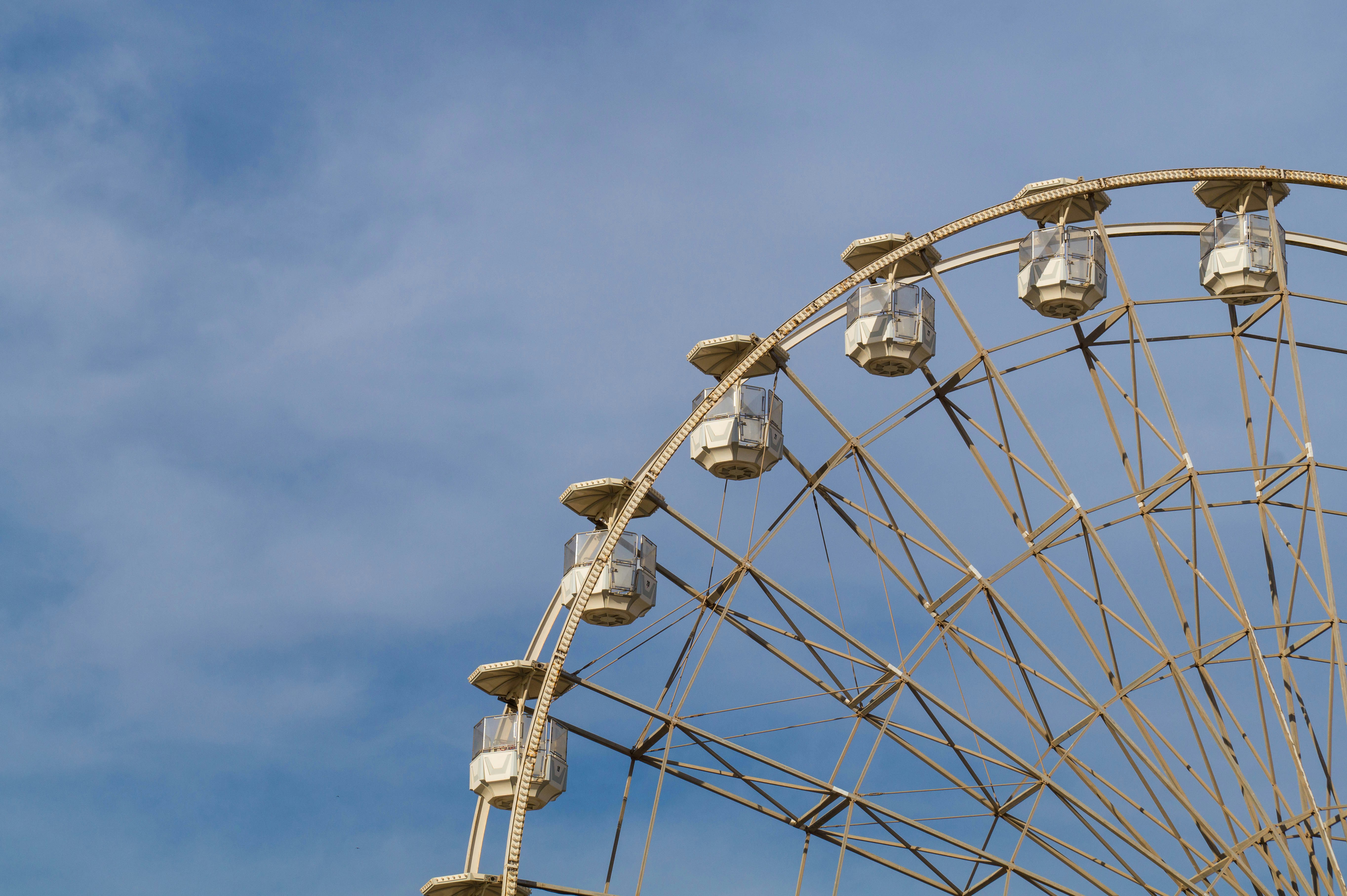Partial view of a Ferris wheel with white gondolas set against a clear blue sky.