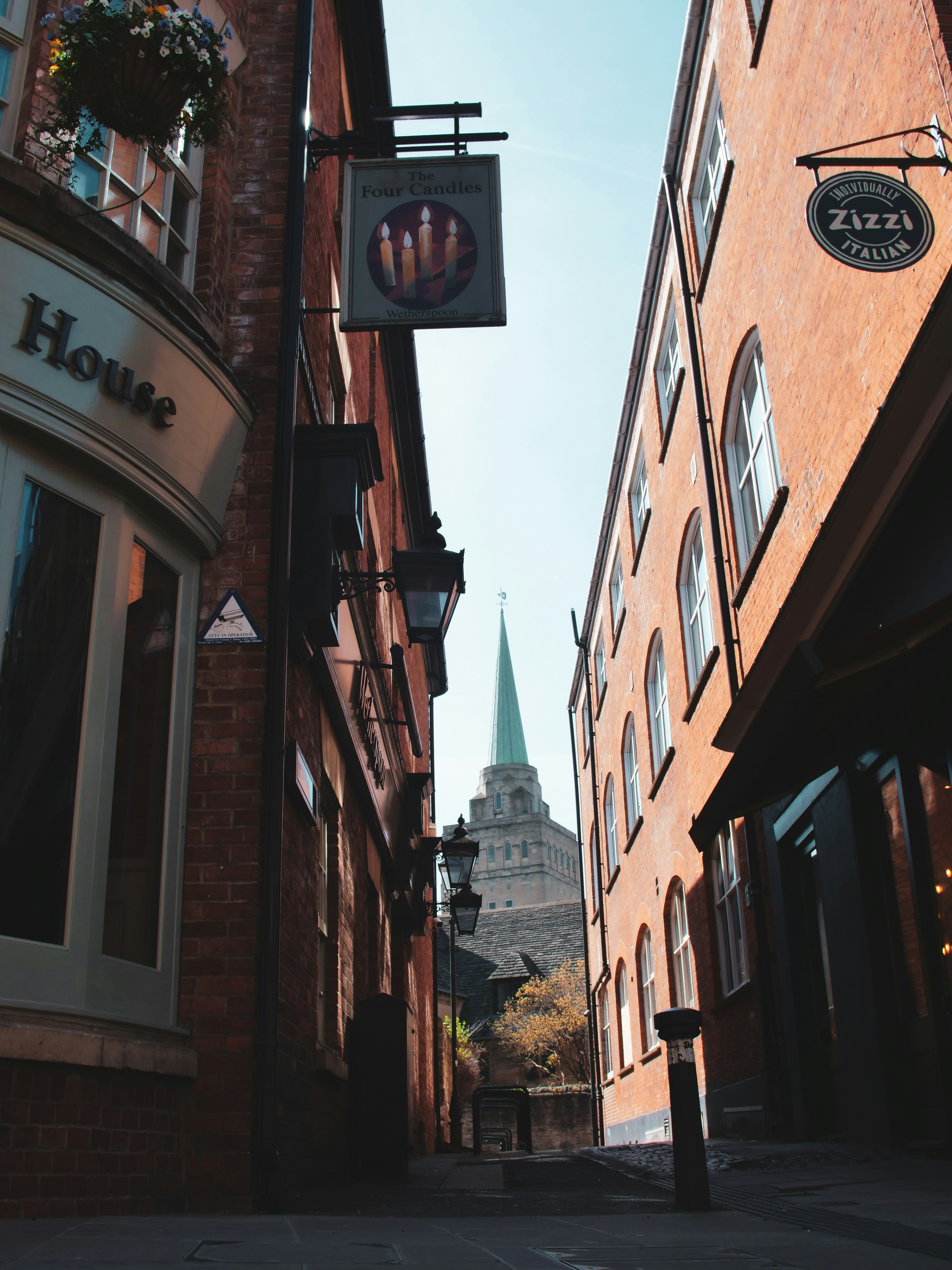 Narrow alleyway framed by brick buildings leading to a distant spire under a clear sky.