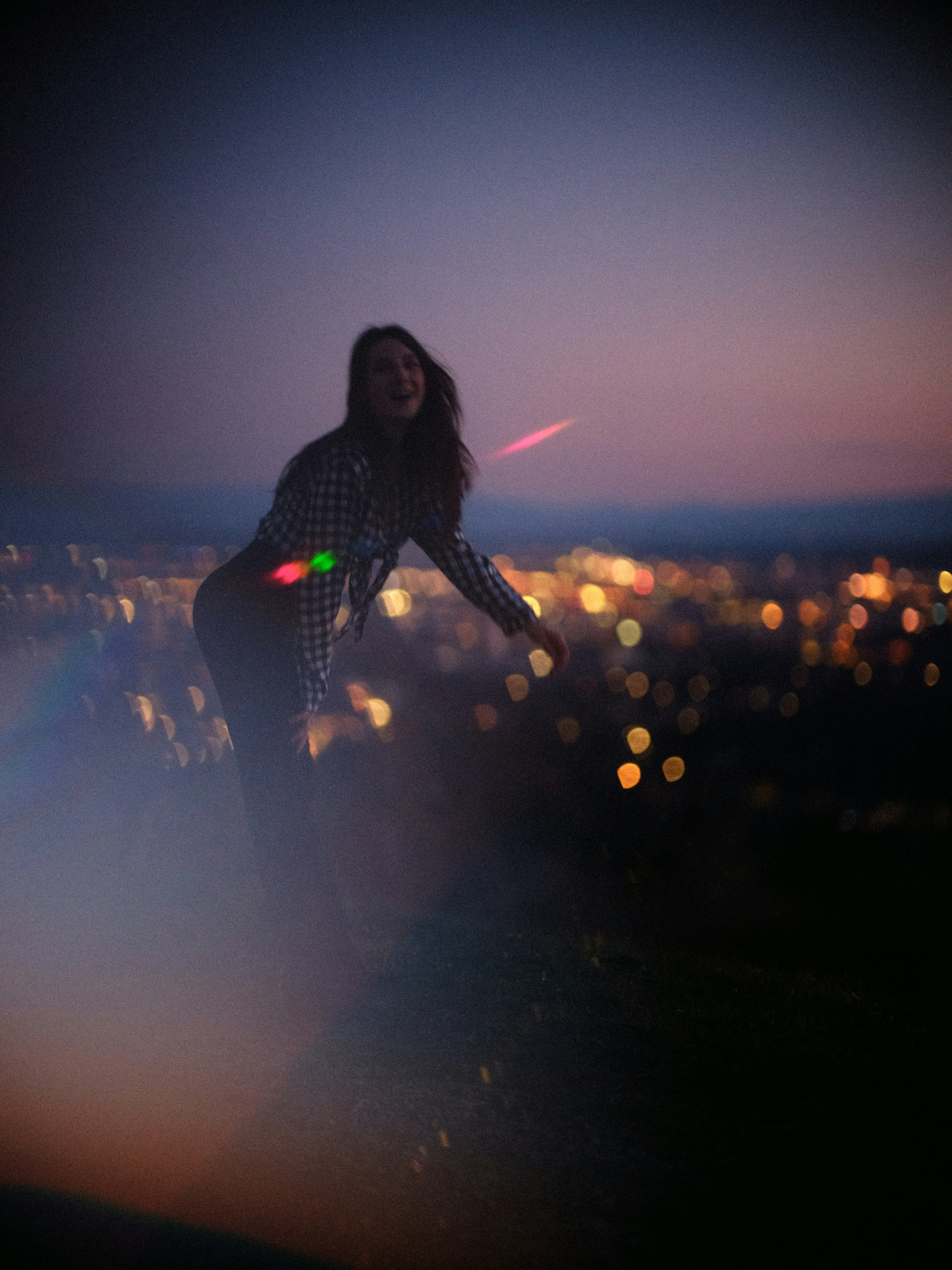 woman dancing over the lights of a city during blue hour night  | woman in black and white polka dot long sleeve shirt standing on the ground during night