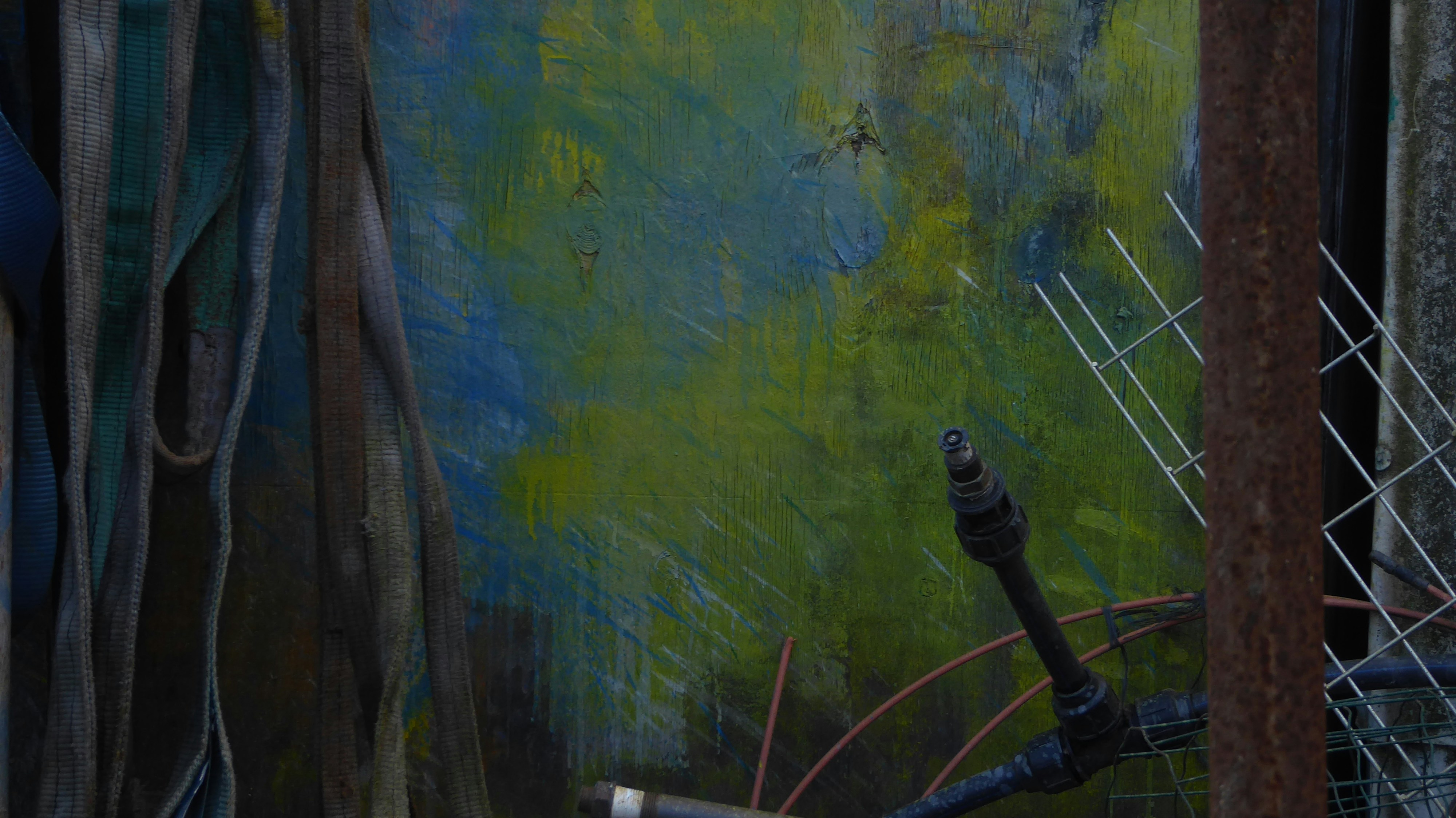 A vibrant blend of green and blue hues with textured elements and industrial materials in the foreground. The composition highlights an intriguing interplay between color and form.