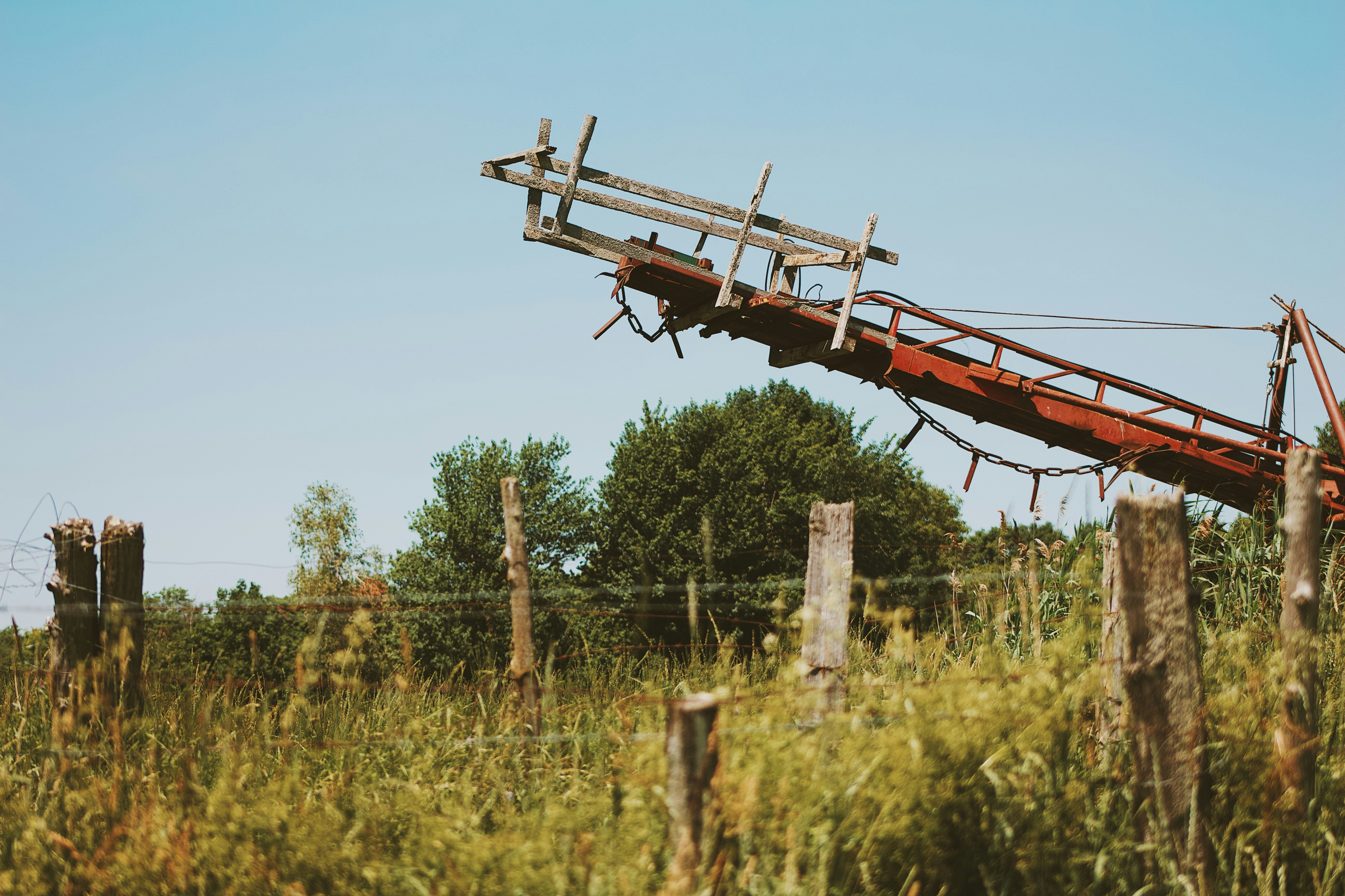 Old agricultural machinery stands amidst overgrown grass under a clear blue sky.