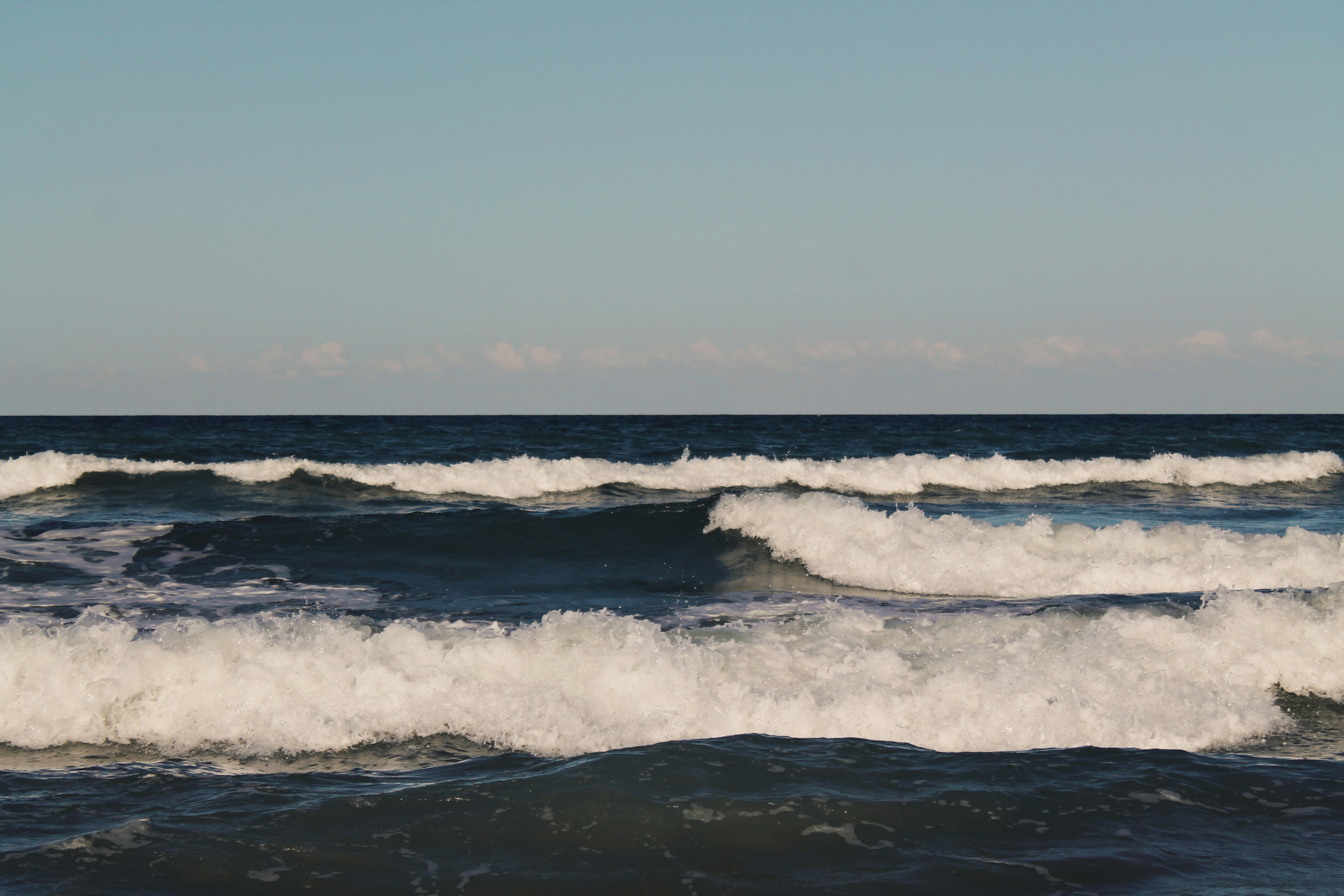 Waves crashing rhythmically against the shore under a clear sky, capturing the essence of coastal tranquility.