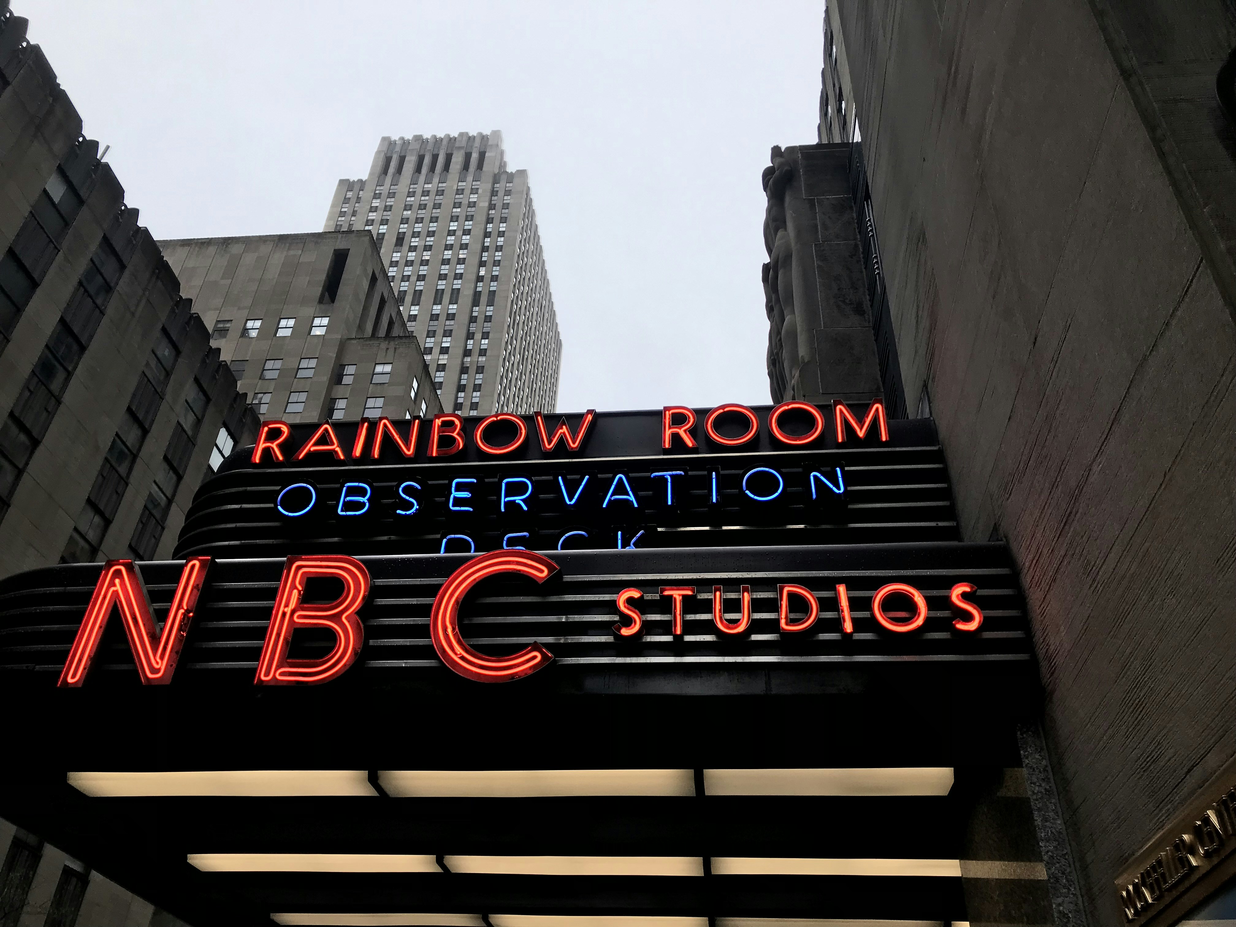 Neon signs for Rainbow Room and NBC Studios against a backdrop of towering skyscrapers.