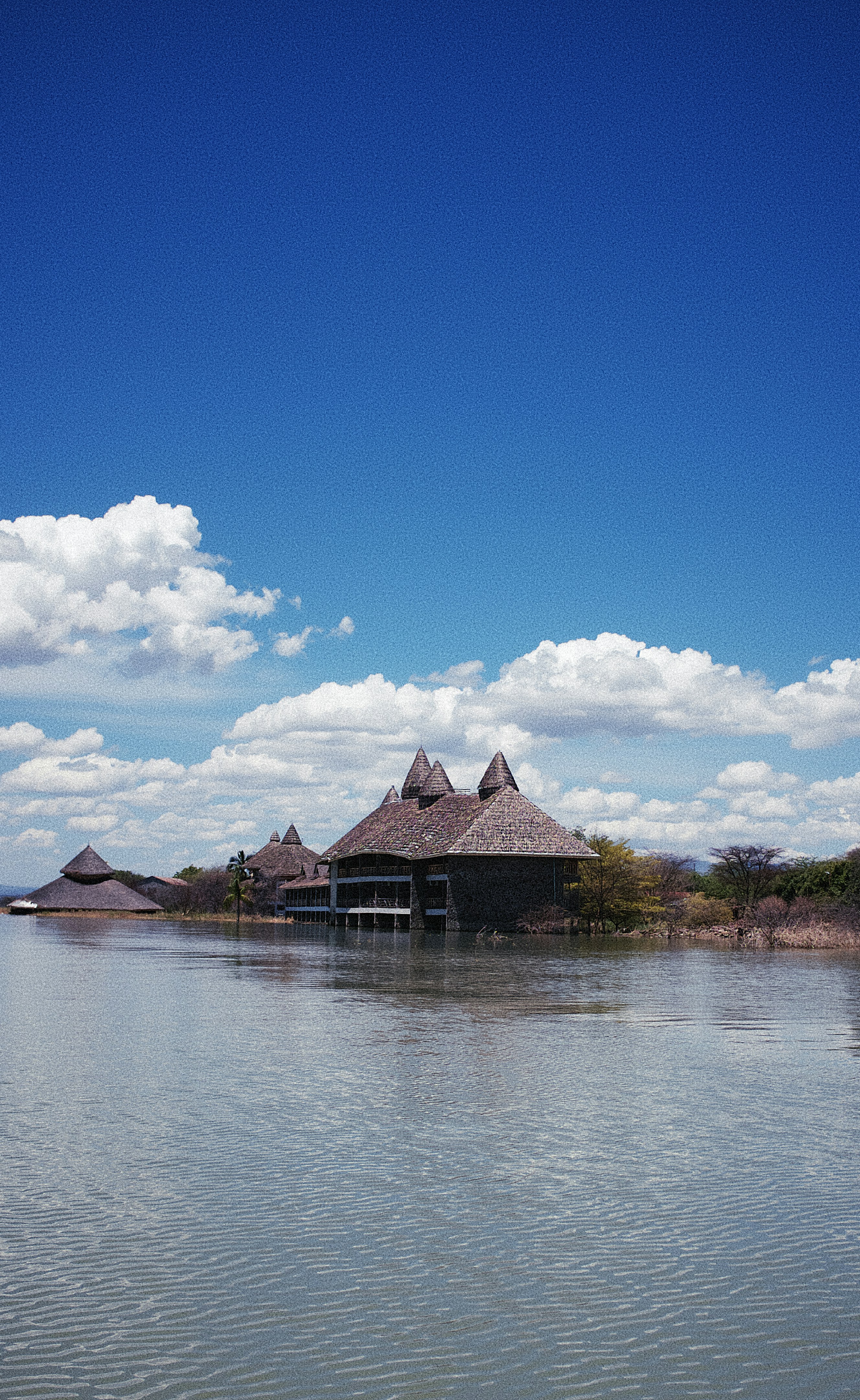 Thatched huts over a calm lake with a bright blue sky and scattered clouds.