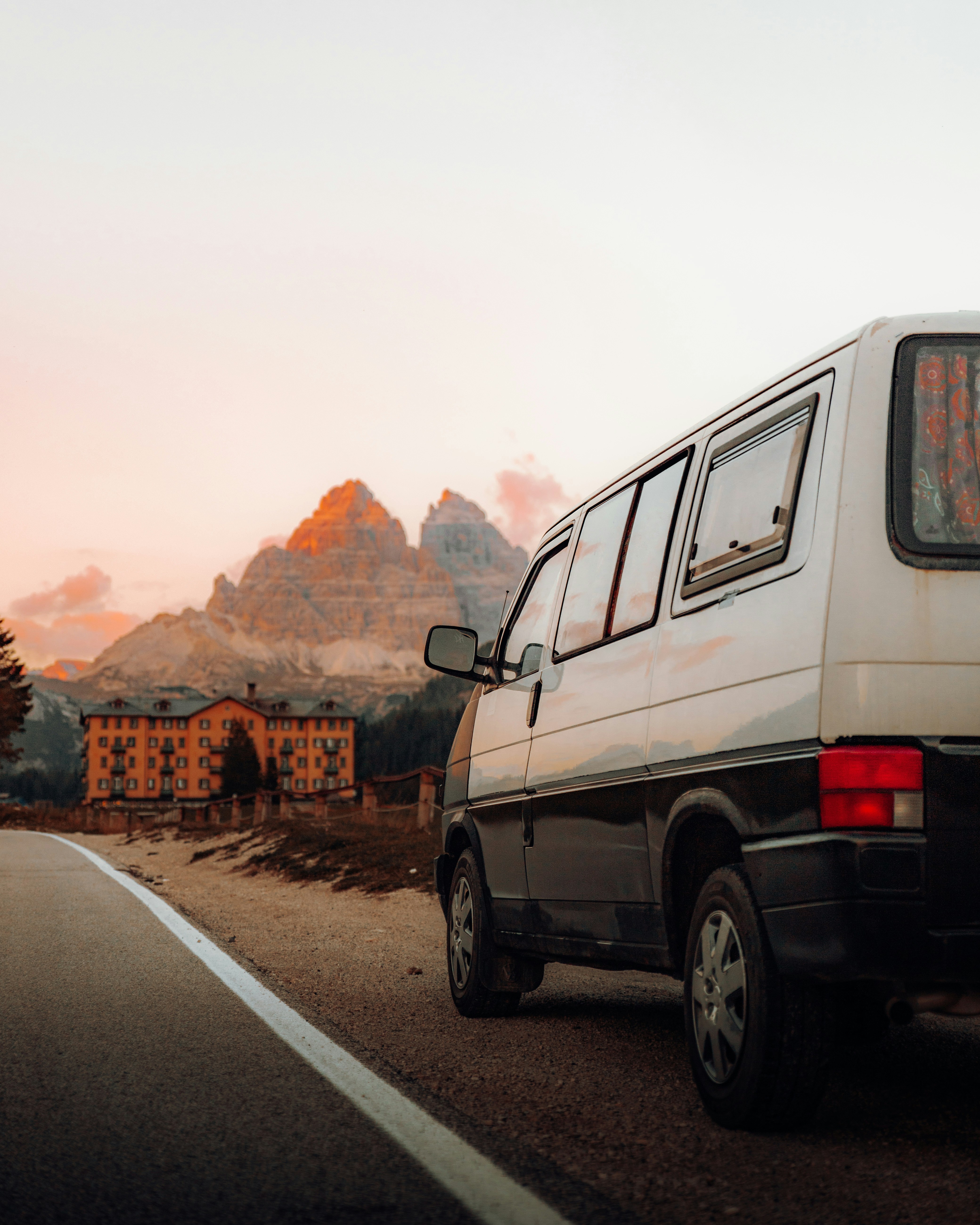 Classic van parked along a winding road with the majestic Dolomite mountains in the background during sunset.