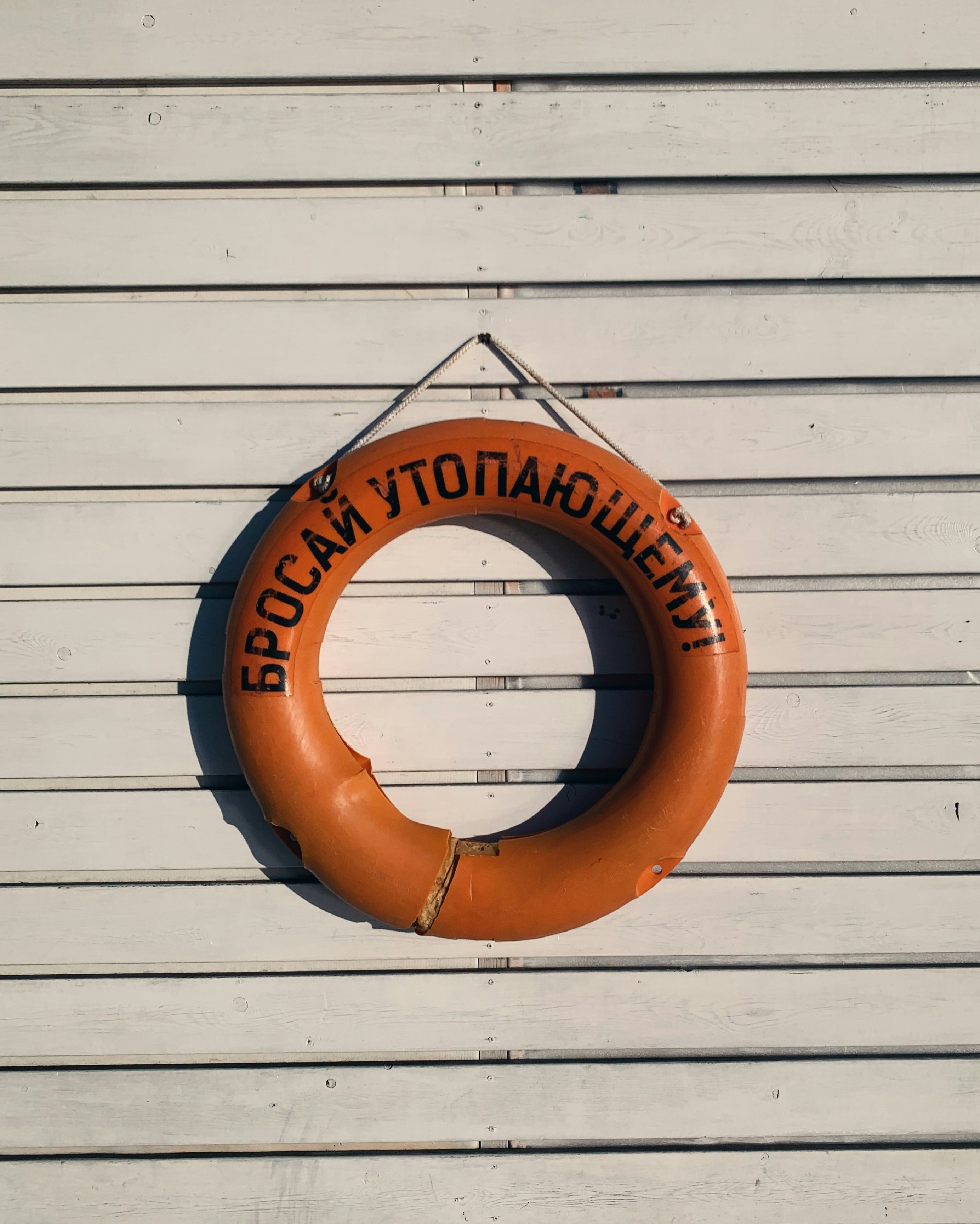 Bright orange lifebuoy mounted on a wooden wall, inscribed with a safety message in Cyrillic. A reminder of maritime safety protocols.