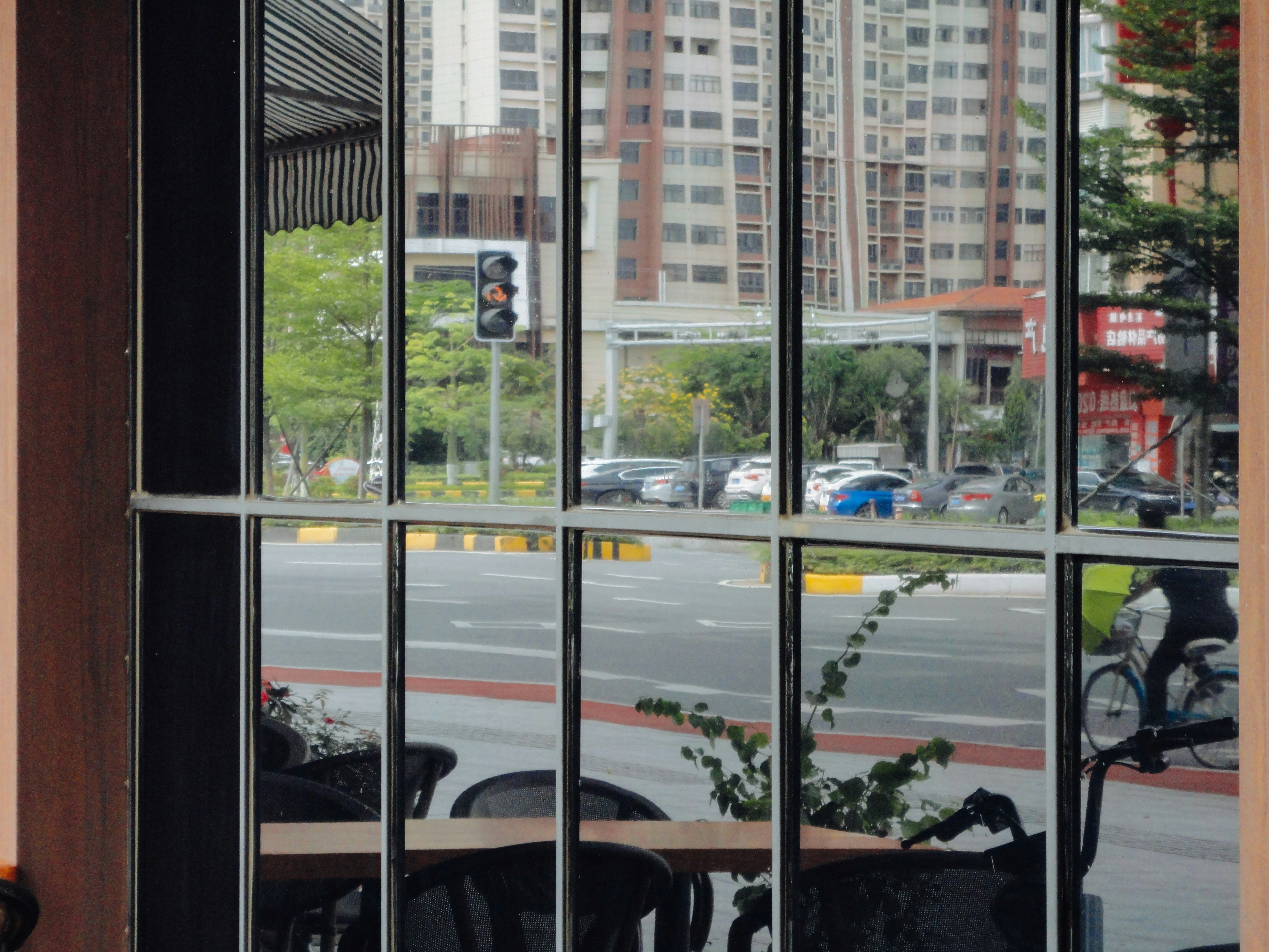 City street framed by window grid, with a cyclist on the right and cars along the road, emphasizing urban reflections.