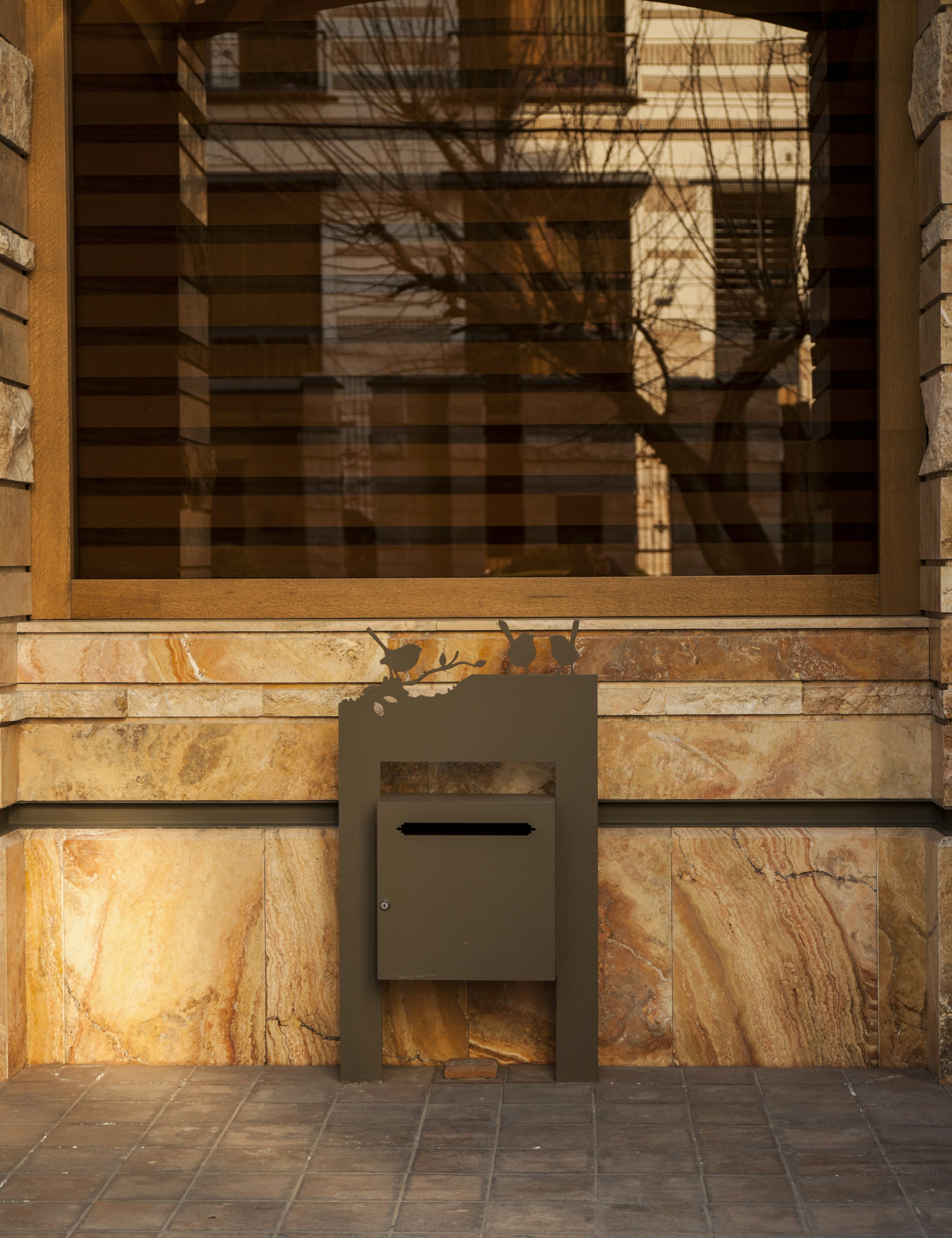 Earthy Façade Inbox: A Bronze Mailbox Framed by Stone and Glass